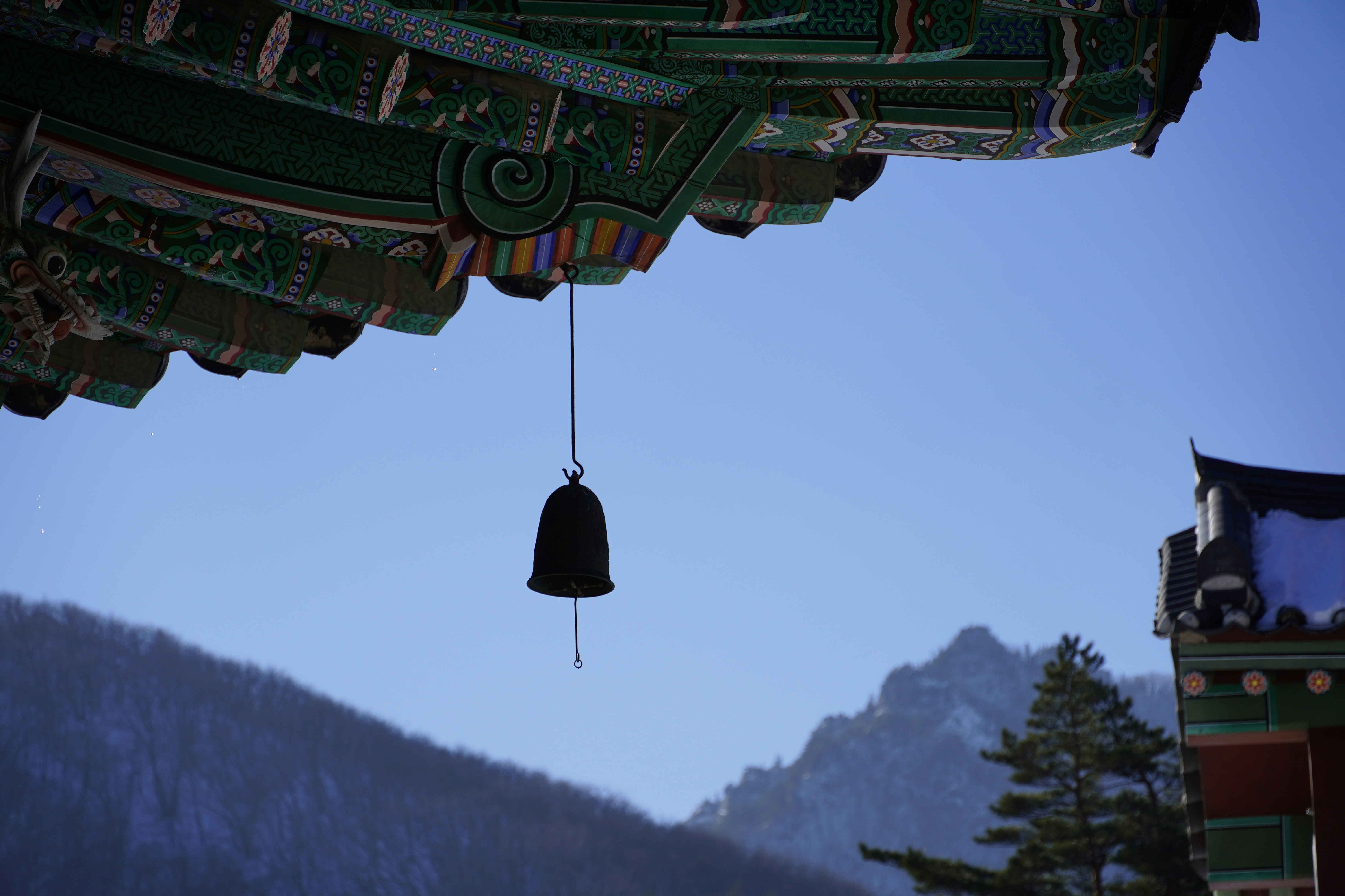 Bell Under Ornate Eaves: Winter Temple Scene with Distant Peaks