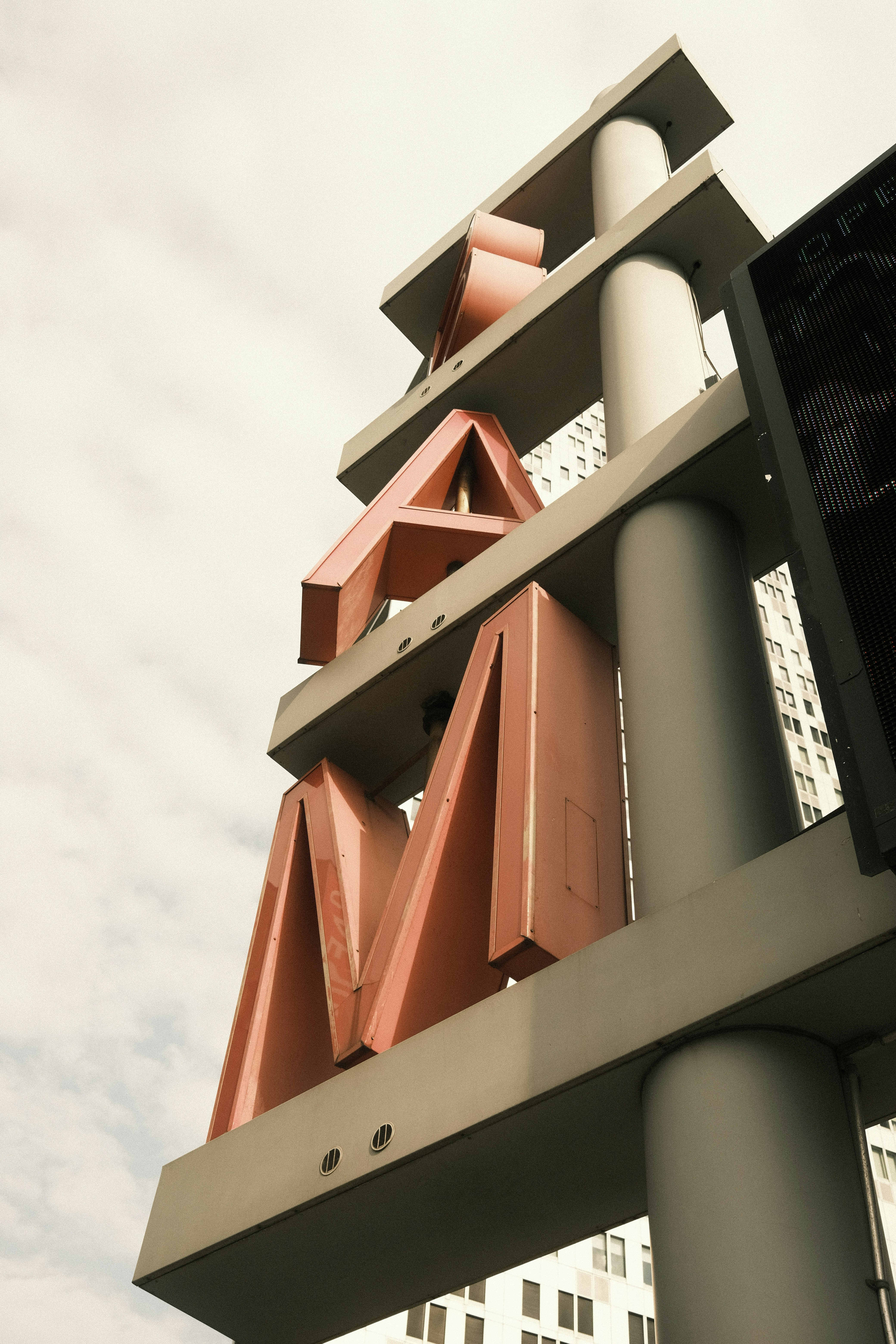 Tilted M Over Steel: Pink Geometry Rising Toward the Sky