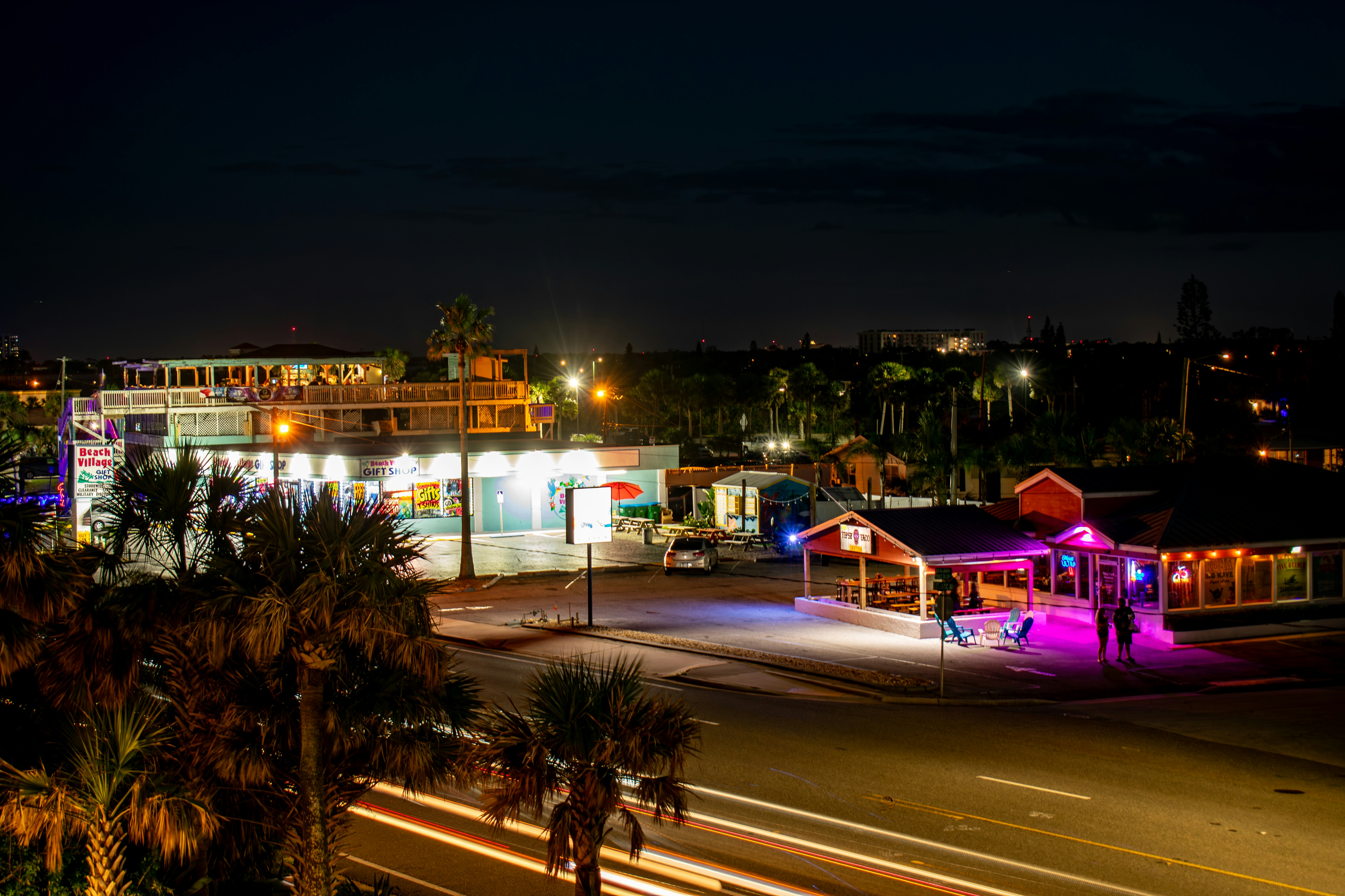 Vibrant city street scene at night with colorful neon lights illuminating buildings and palm trees.