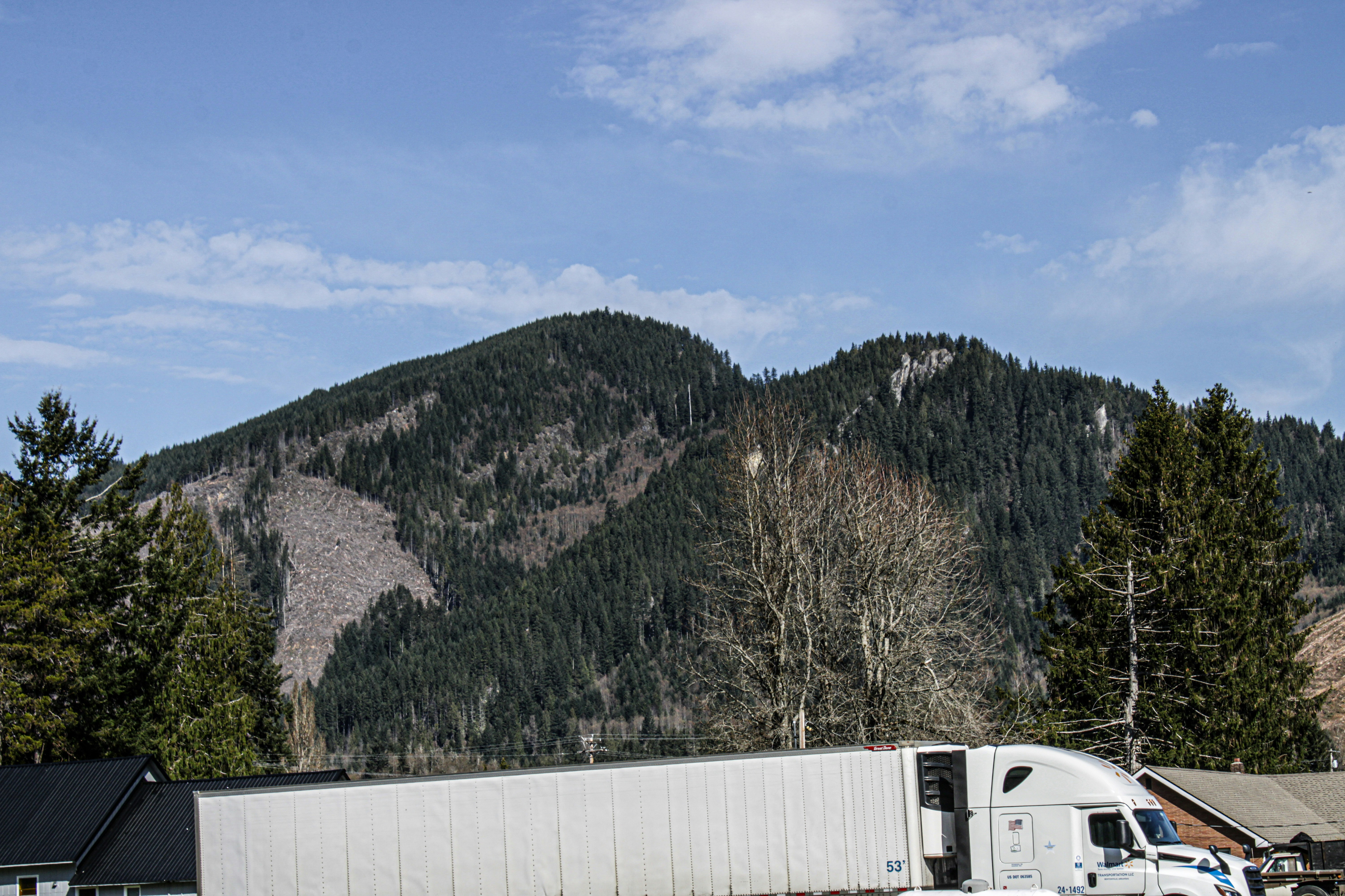 A large white truck parked in front of a backdrop of lush mountains and clear blue skies, showcasing the harmony between nature and industry.