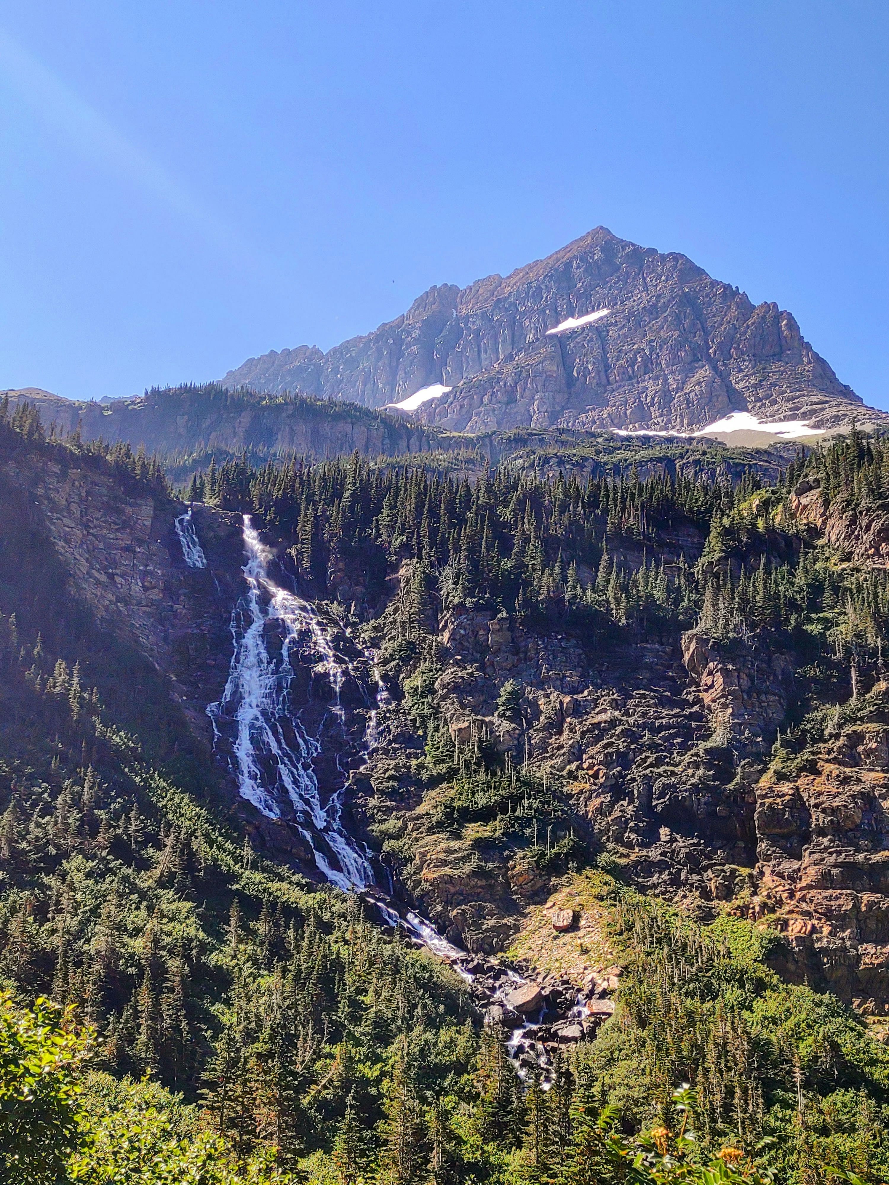 Whispering Falls Along Pine-Clad Cliffs Beneath a Snow-Dusted Summit