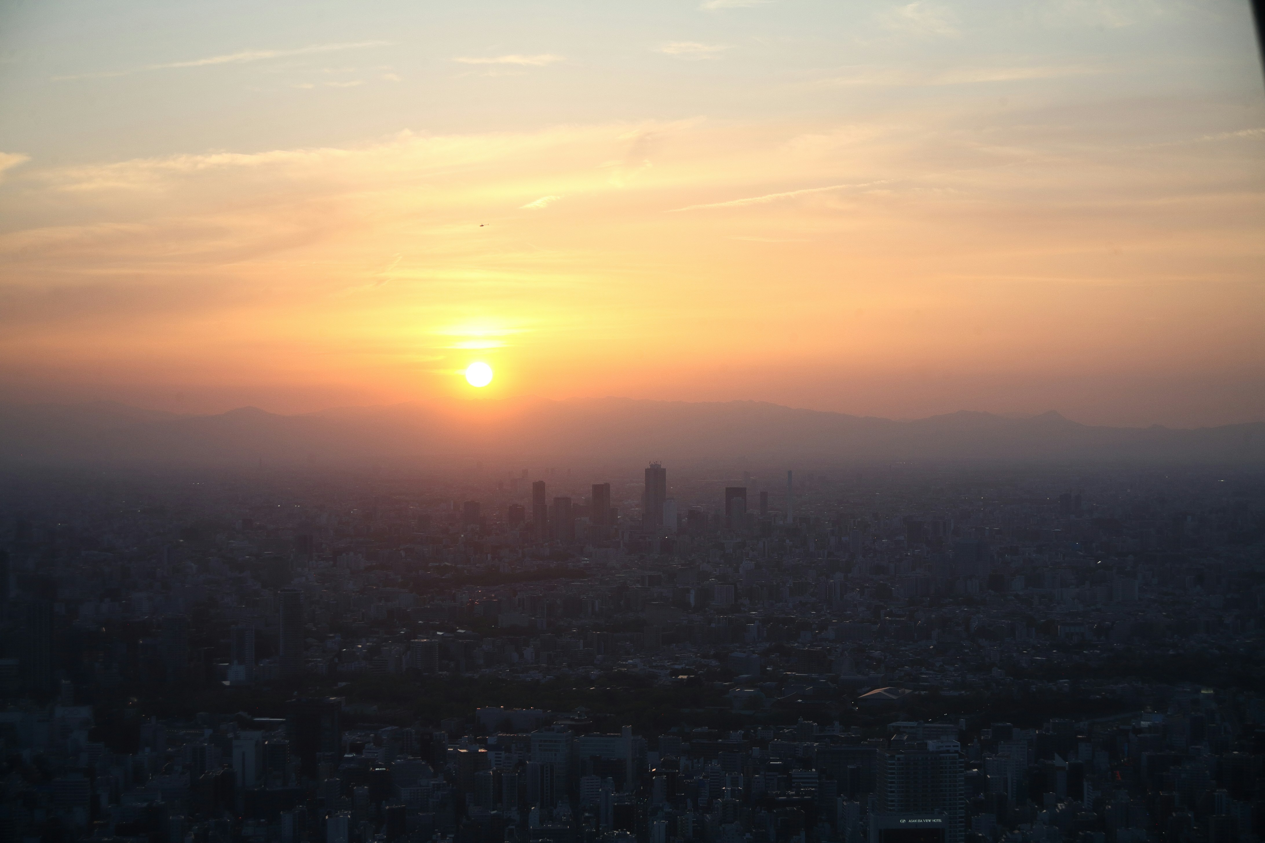 Sunset casting warm hues over a sprawling cityscape with distant mountains.