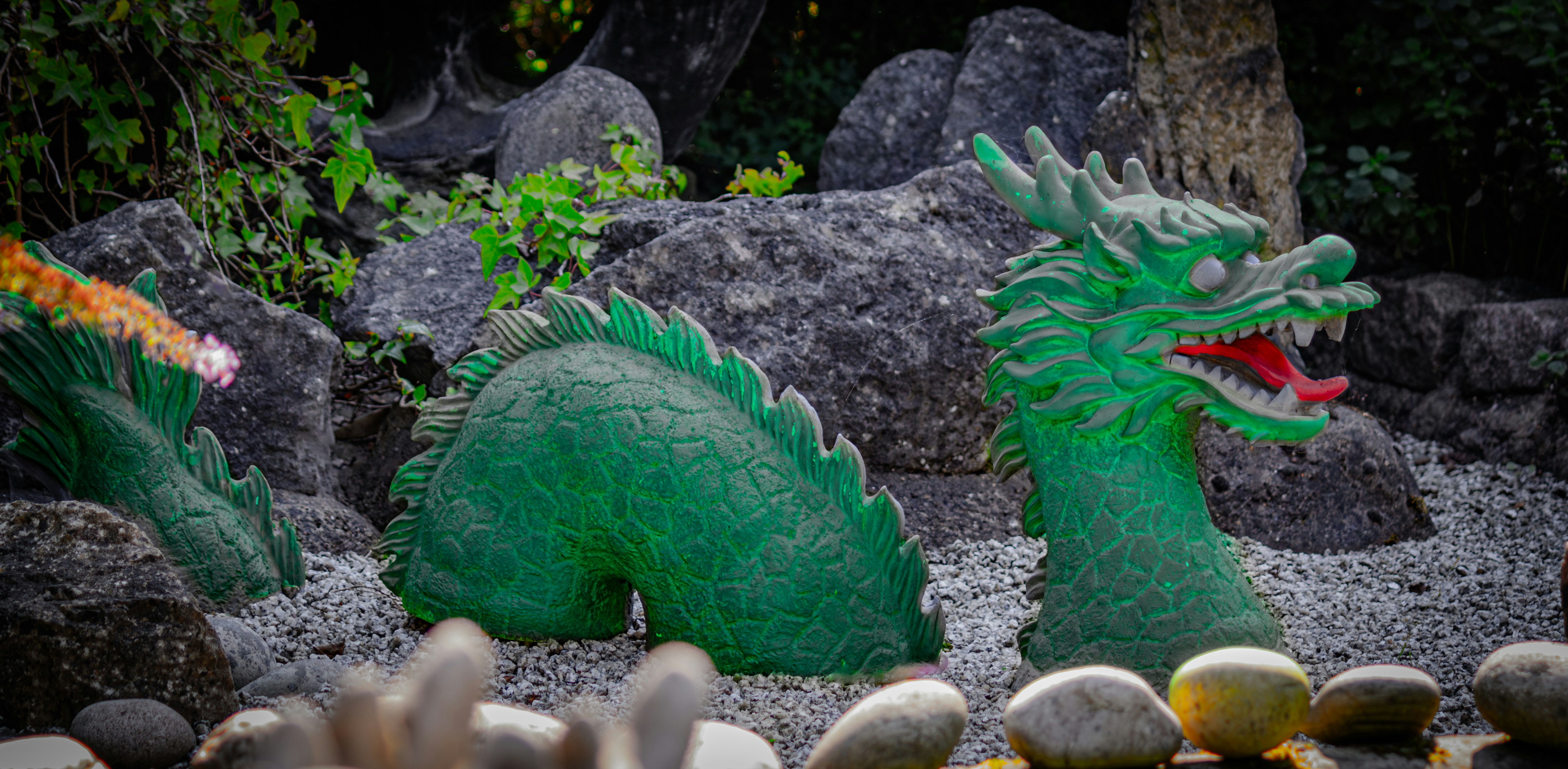 A couple of green statues sitting on top of a gravel field photo – Free ...