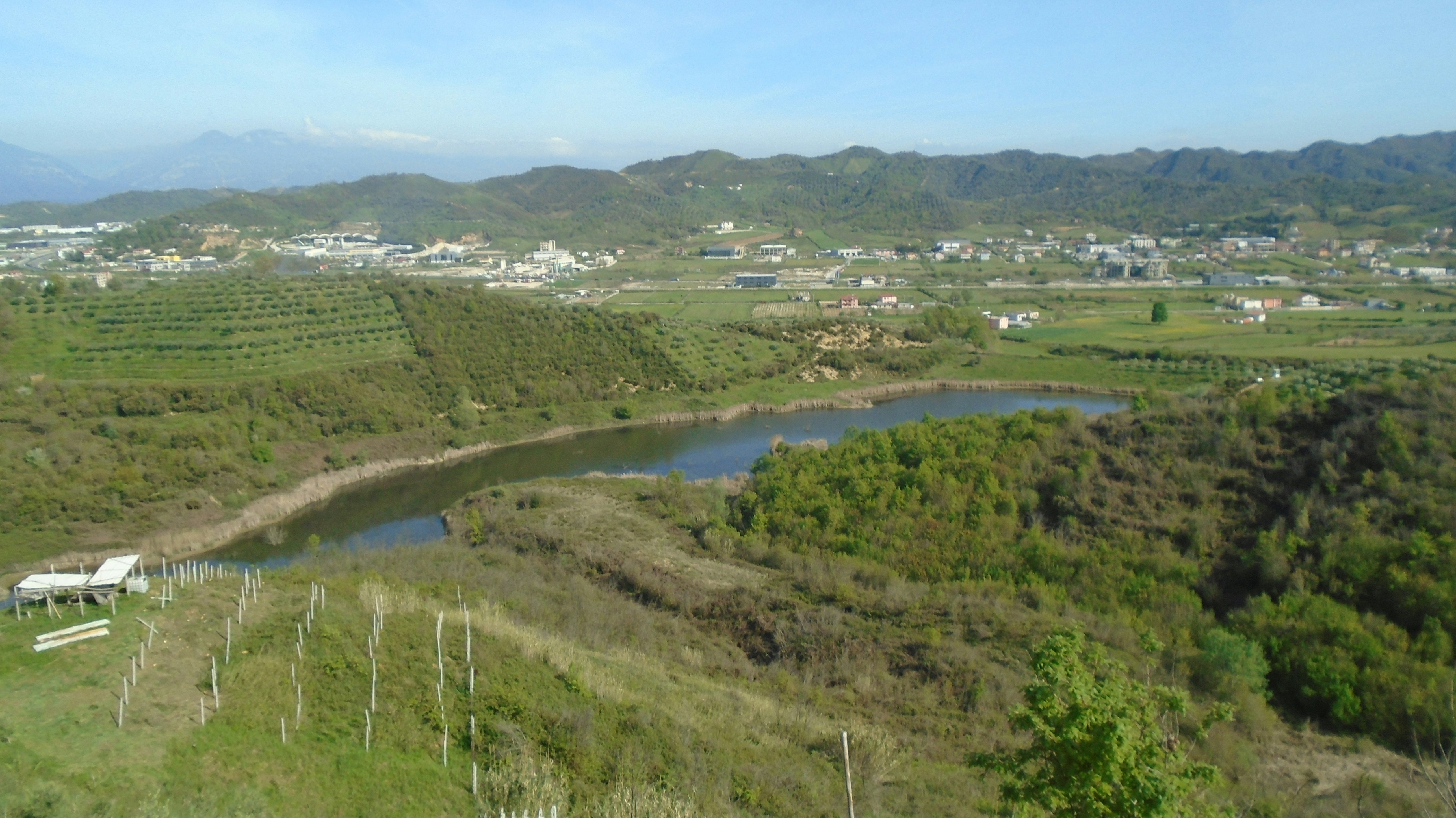 A winding river meanders through lush greenery, framed by rolling hills and distant mountains under a clear sky.