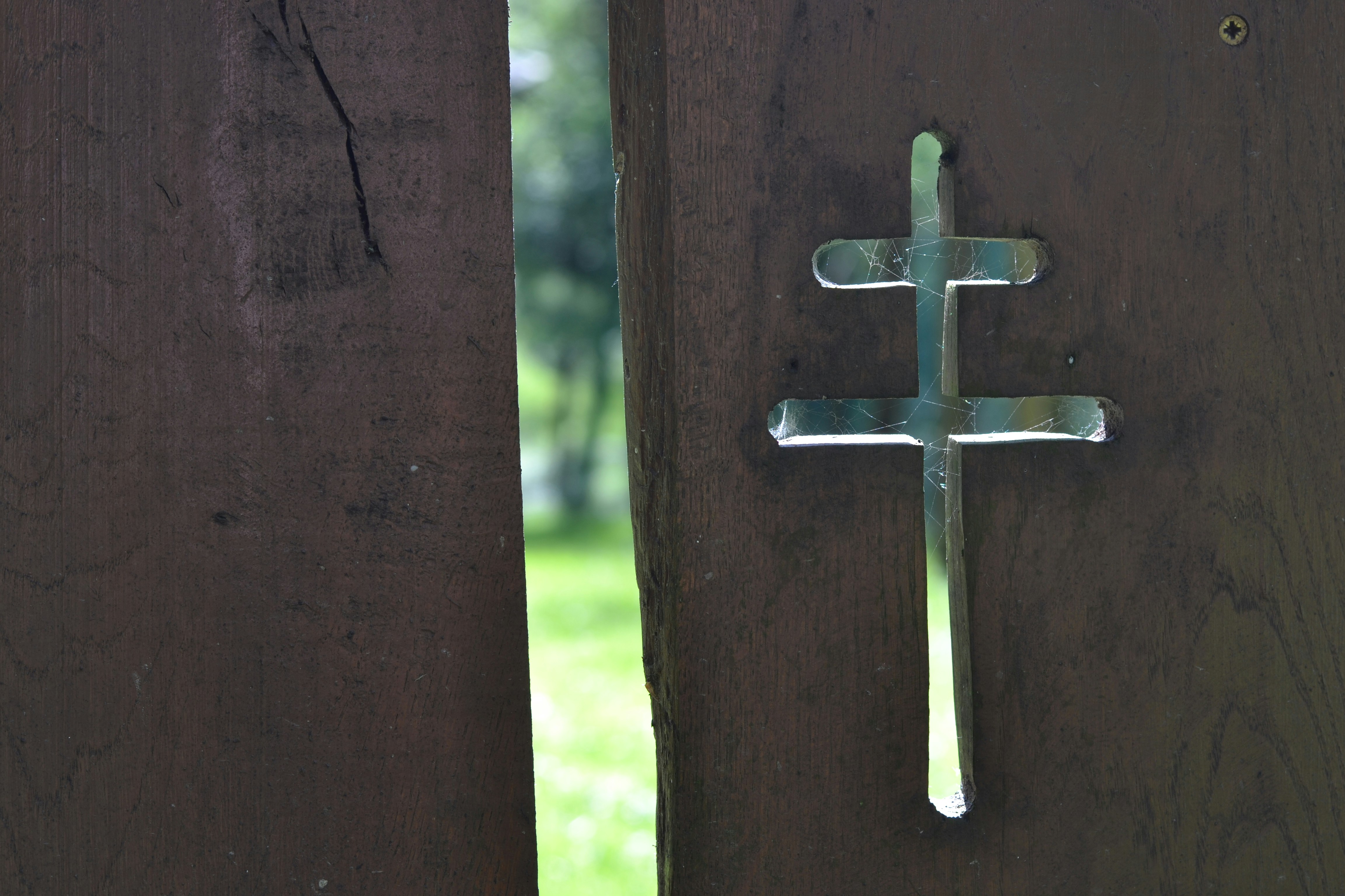 A metal cross cutout in a wooden gate, framed by the surrounding greenery, evokes a sense of tranquility and contemplation.