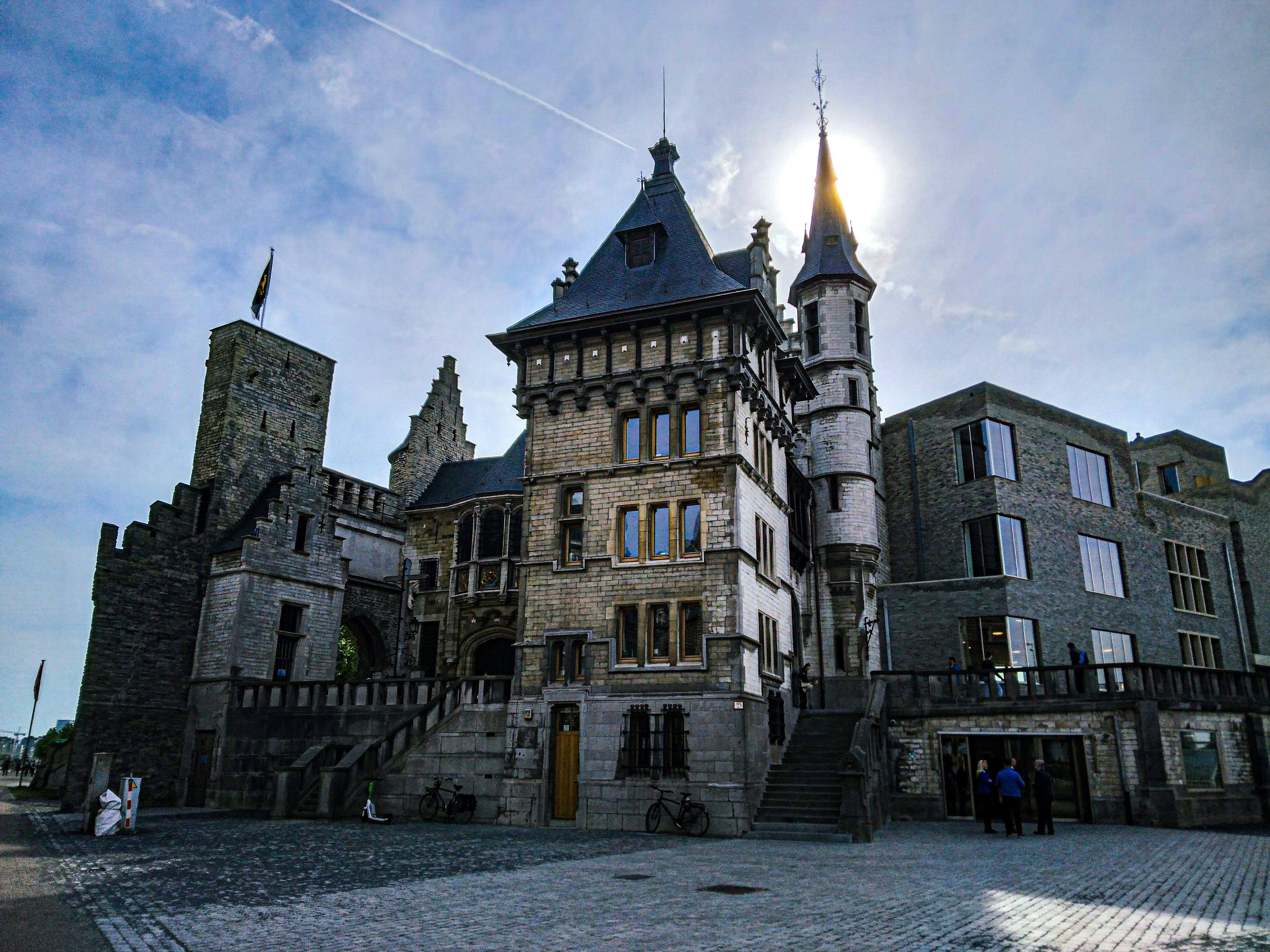 Historic stone castle with turrets and a sunlit spire against a partly cloudy sky.