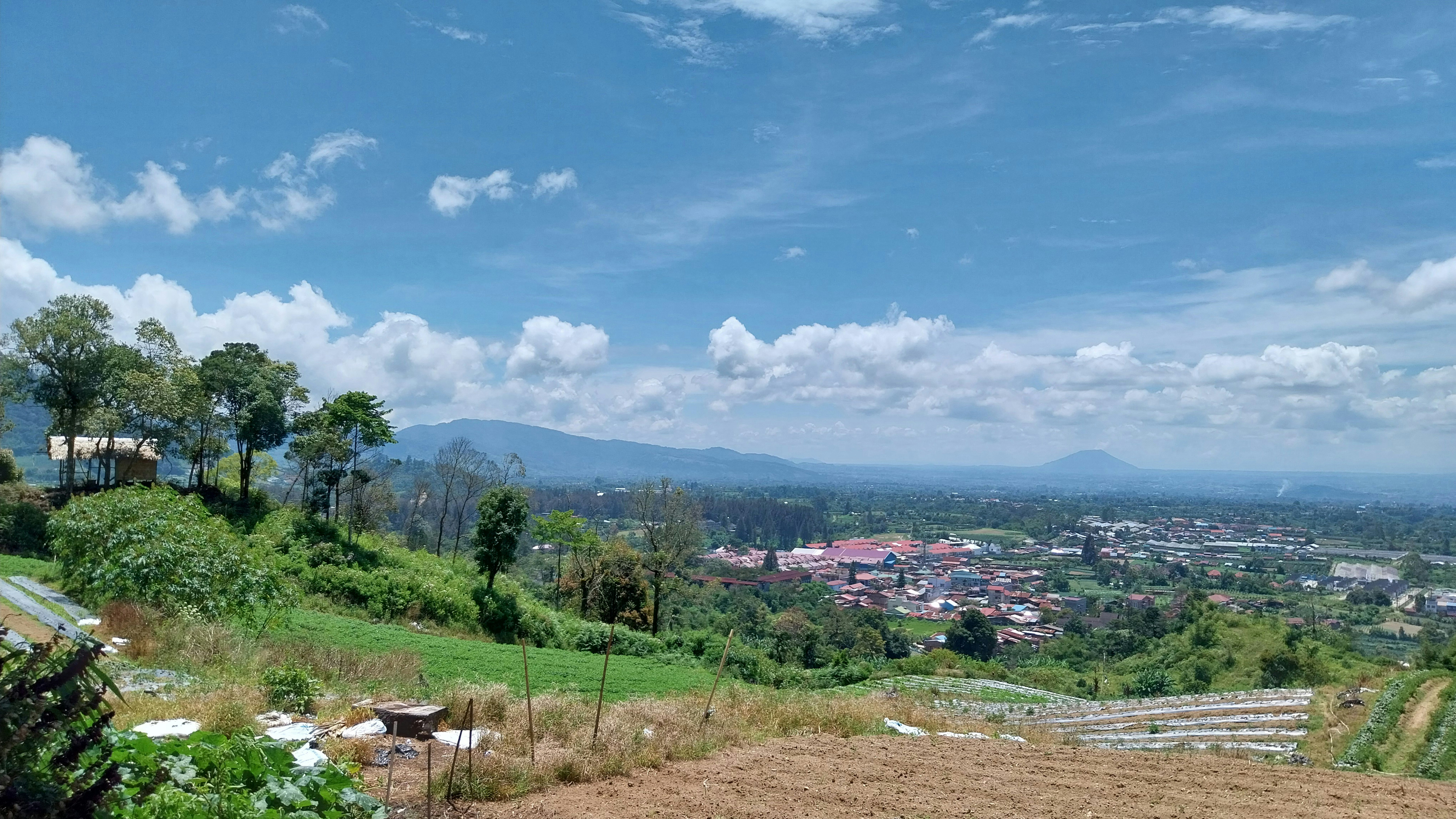 Lush green hillsides overlooking a sprawling town below, framed by distant mountains under a bright blue sky.