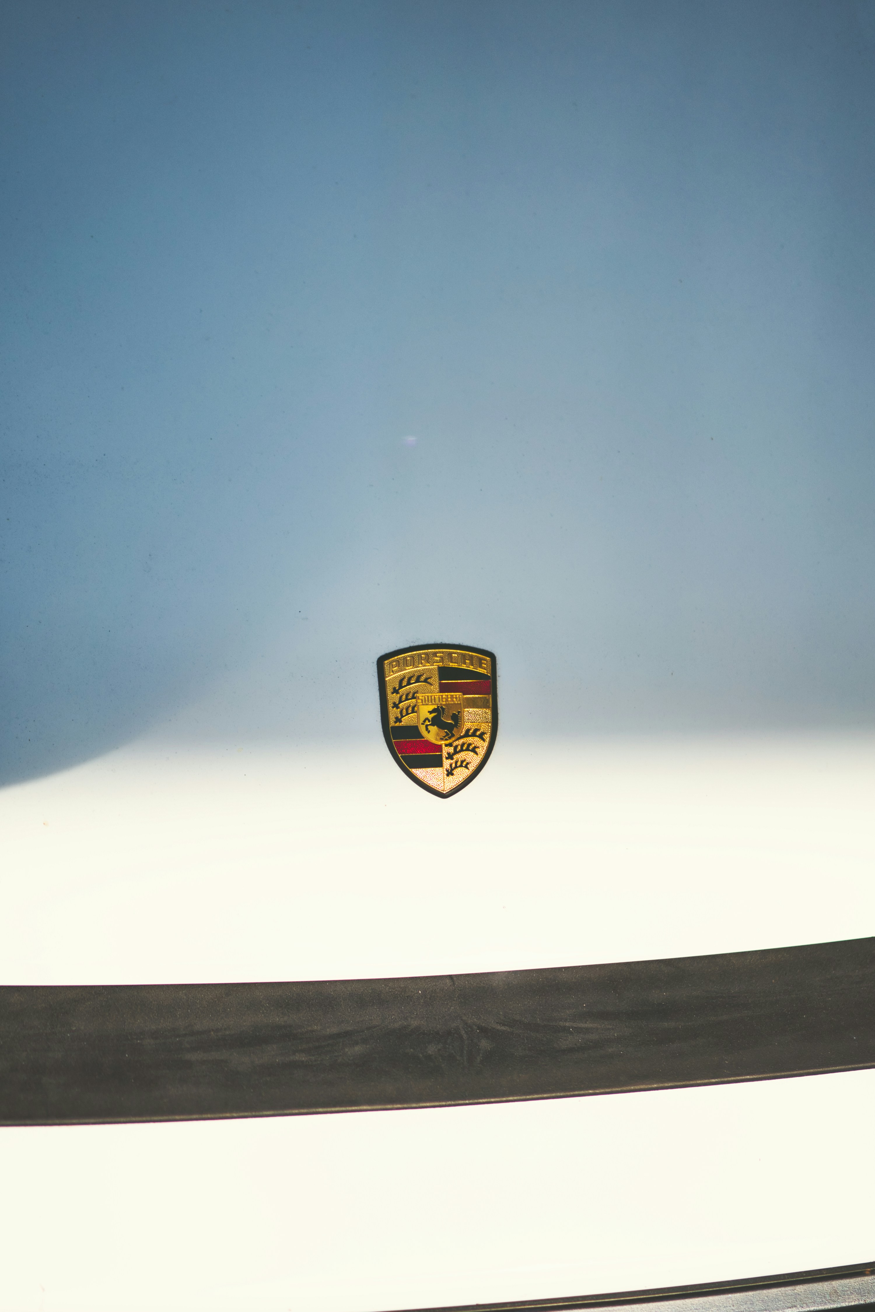 Porsche Crest Against a Quiet Blue Sky: Minimalist Hood Portrait