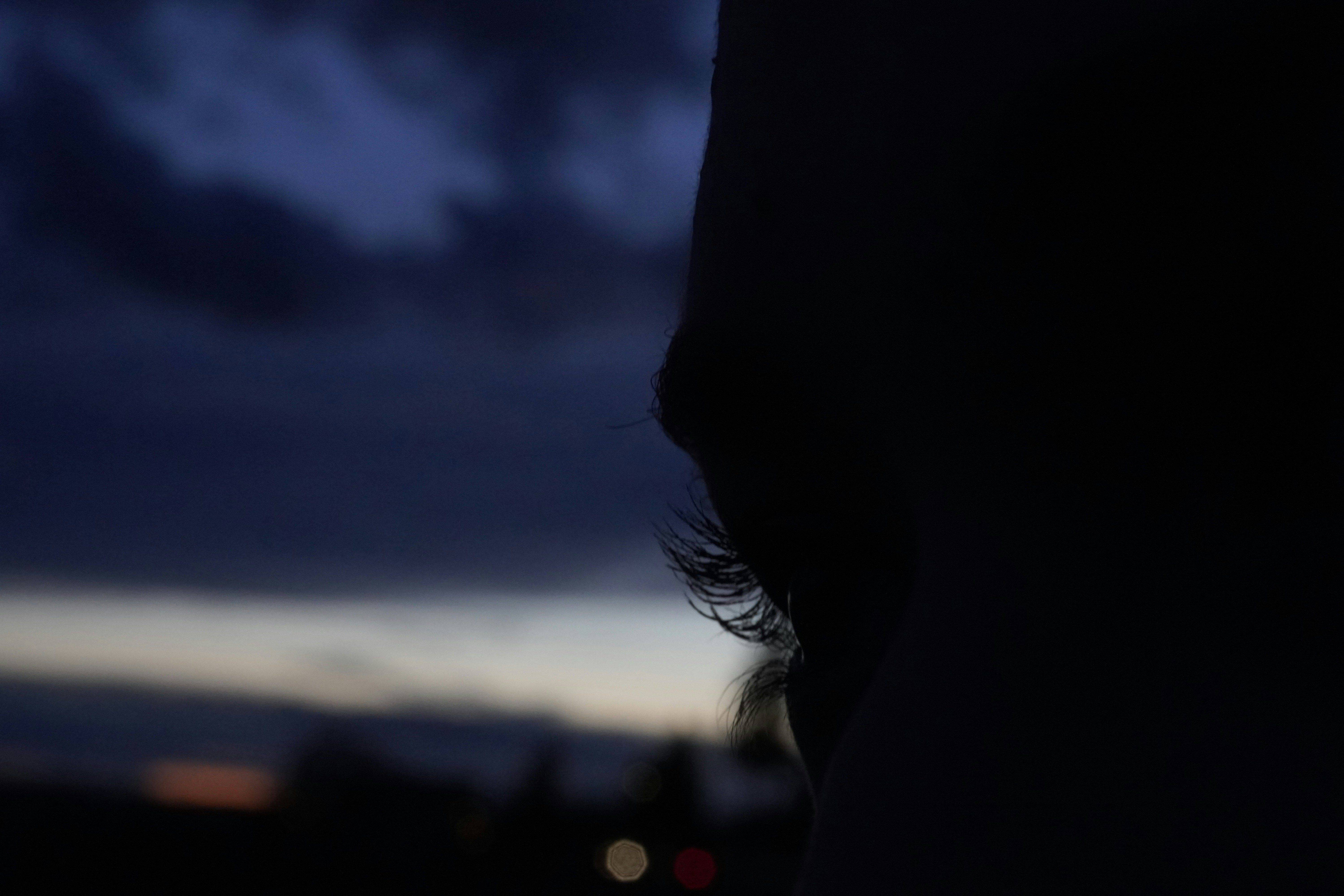 A close-up silhouette of a person's profile, framed against a twilight sky with hints of color emerging on the horizon.