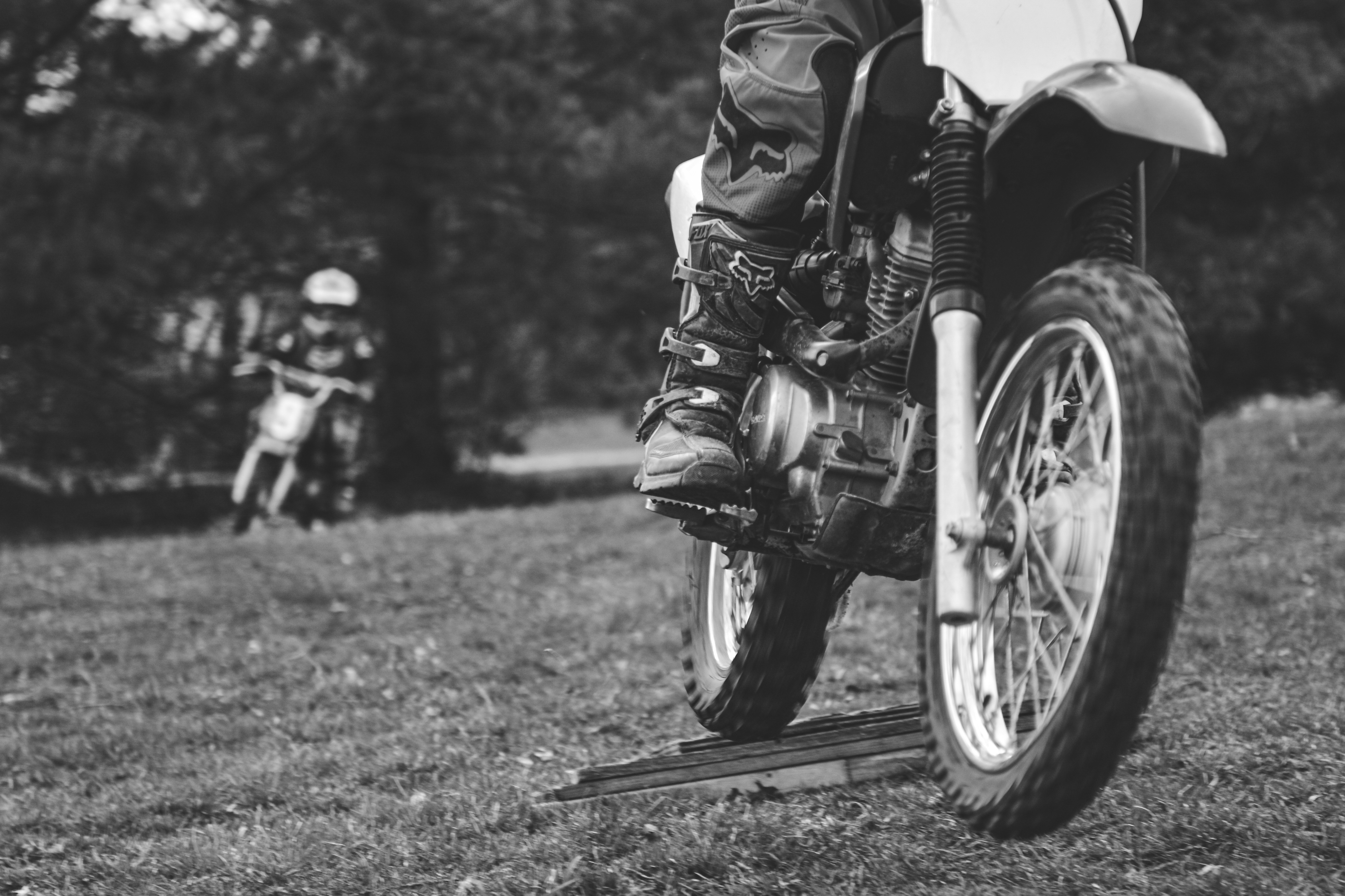 Motorcyclist riding across a grassy field with another bike in the background.