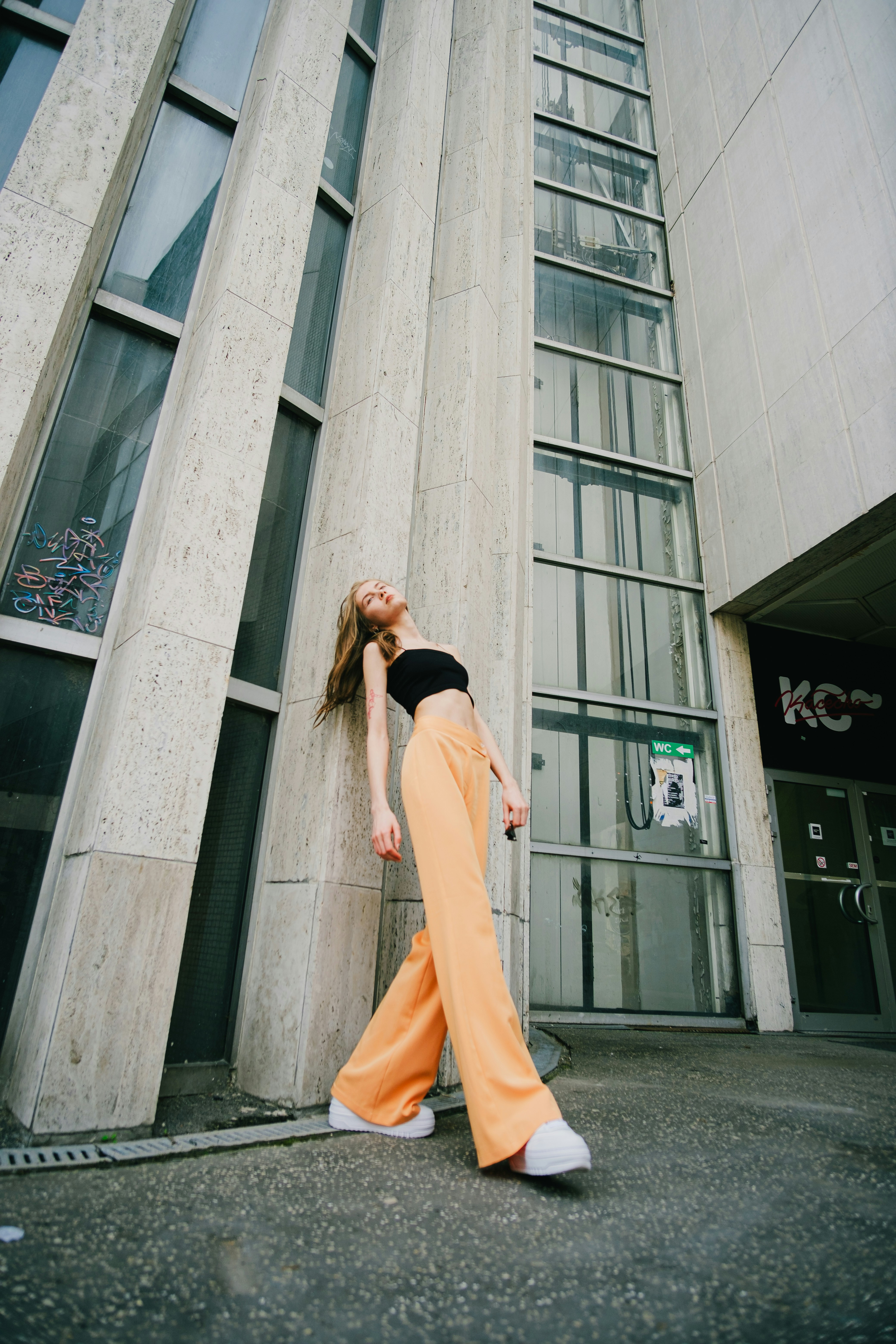 Urban Pose: Long Orange Trousers Against Concrete Vertical
