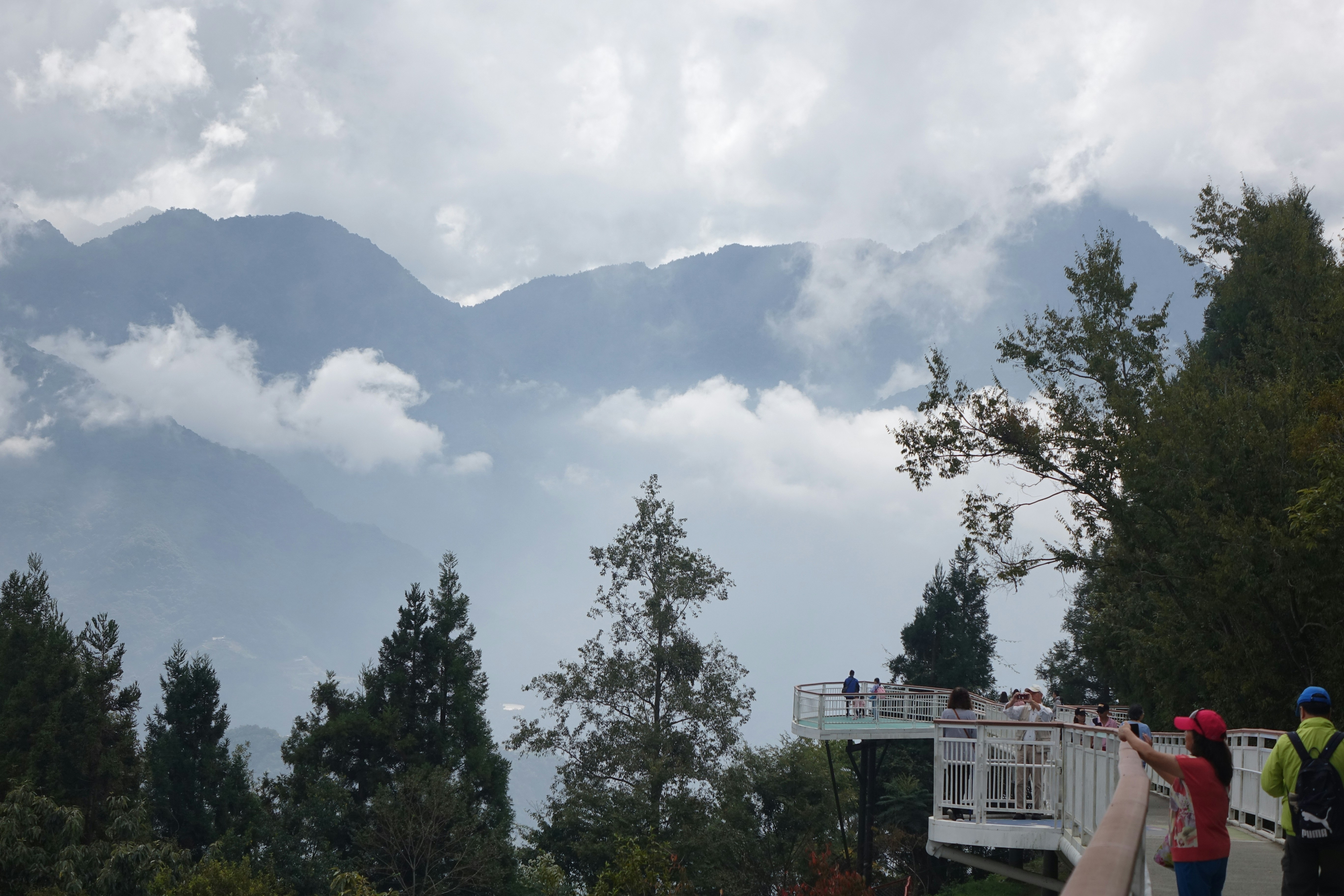 Distant mountains shrouded in clouds with people observing the view from a scenic overlook.
