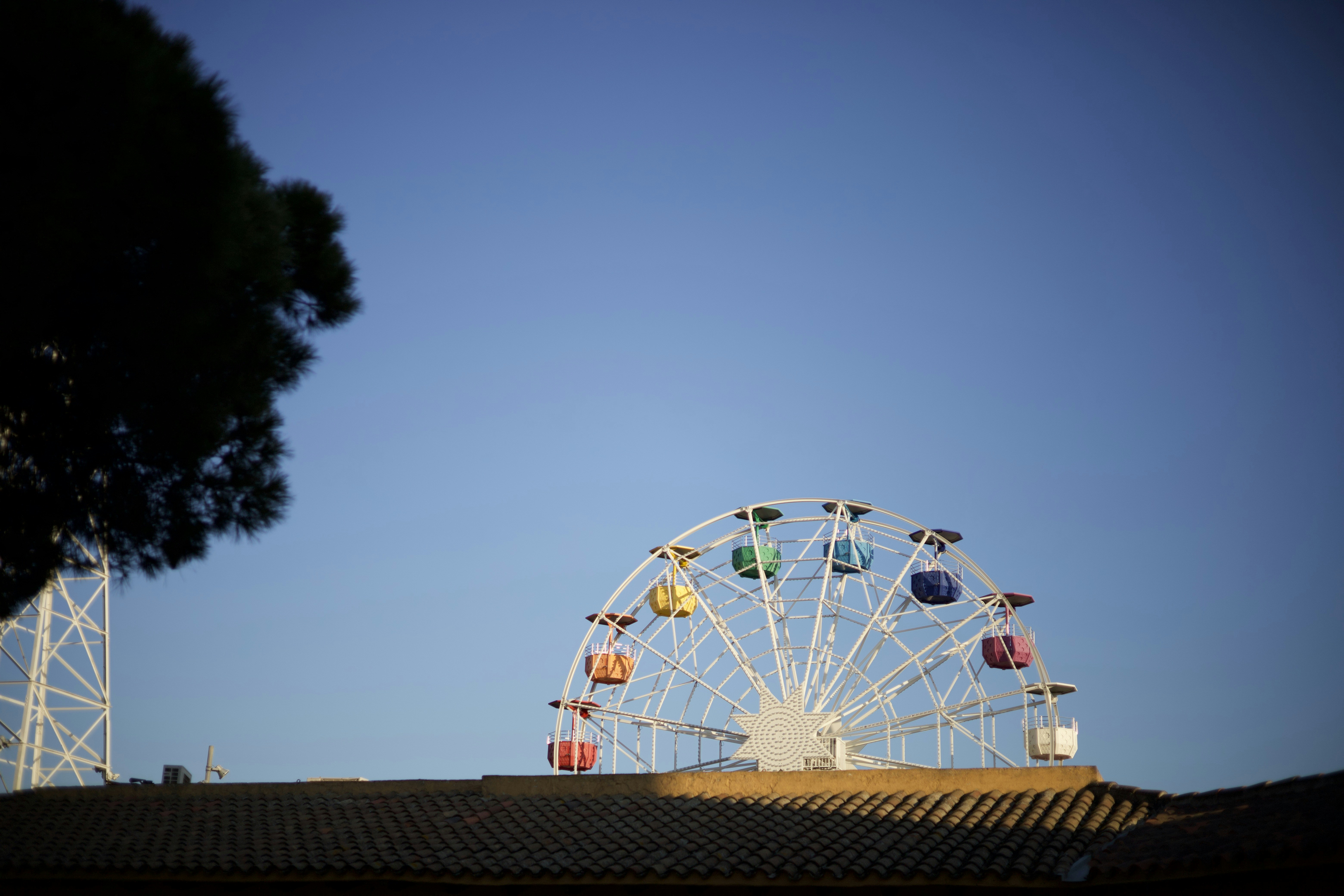 Colorful Ferris Wheel Above a Roofline Under a Clear Blue Sky
