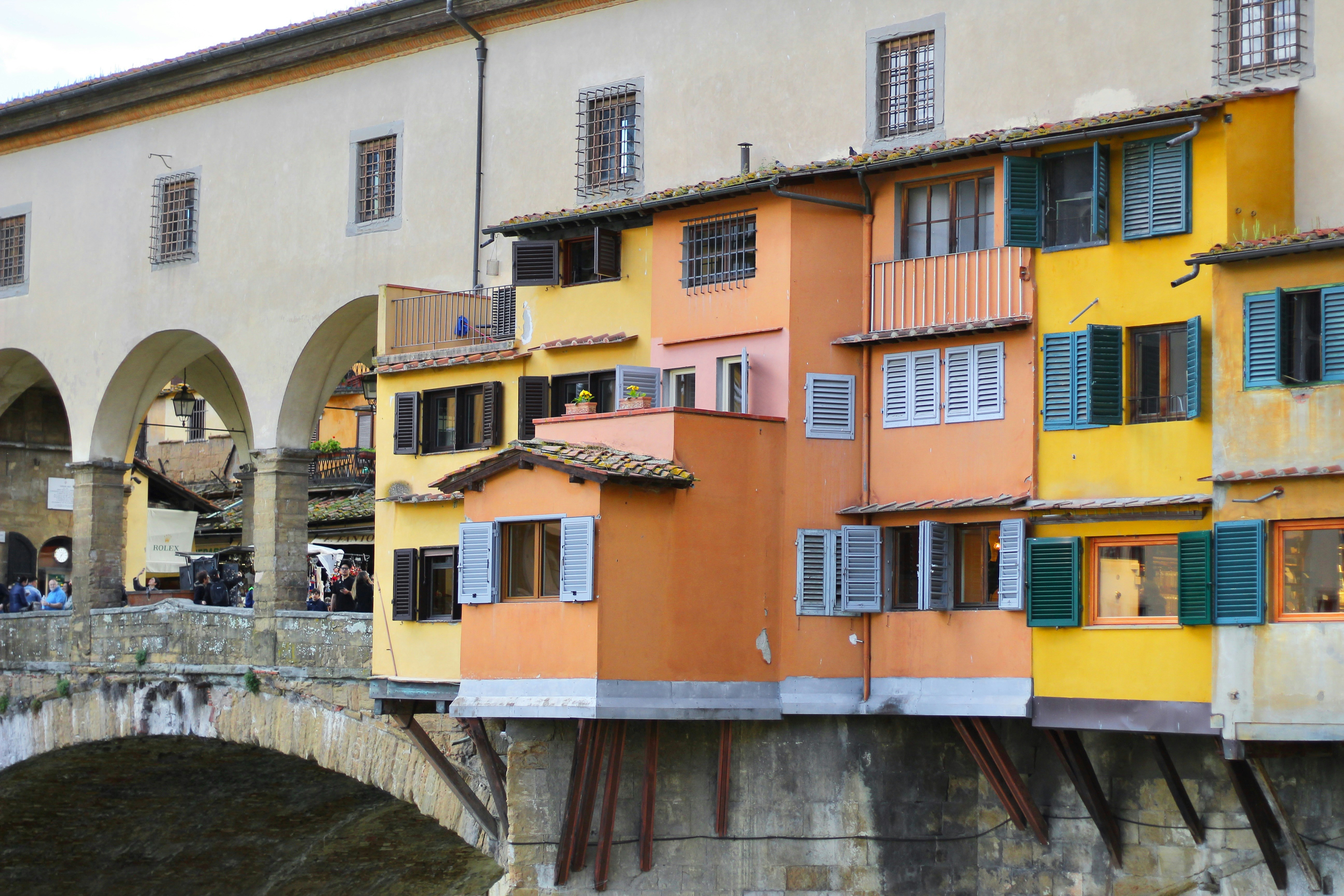Colorful buildings perched over the Arno River, showcasing traditional Italian architecture with open windows and vibrant hues.