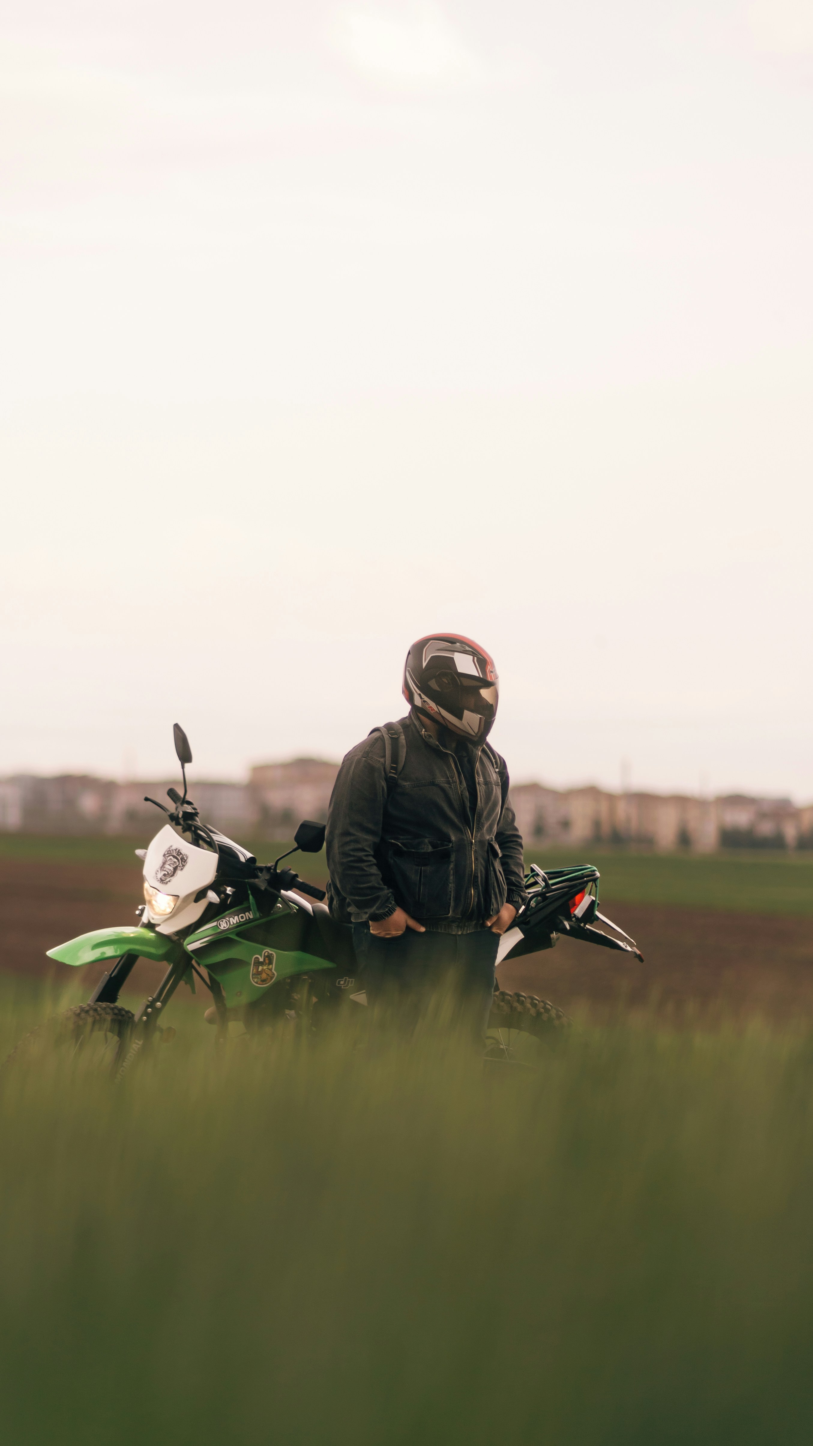 Dusk Pause: A helmeted rider beside a green dirt bike in a quiet field