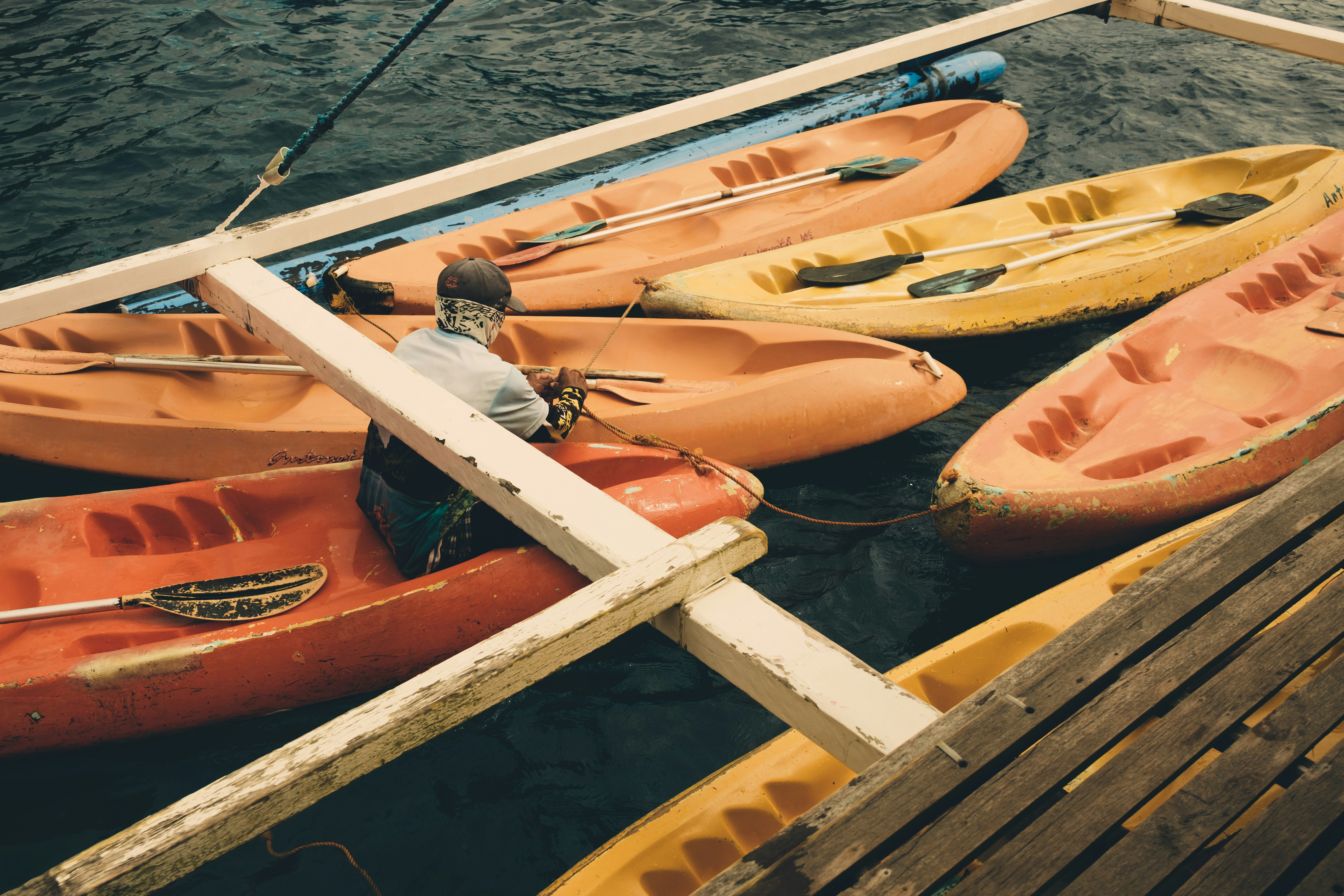 Person arranging colorful kayaks tied to a wooden dock over calm water.