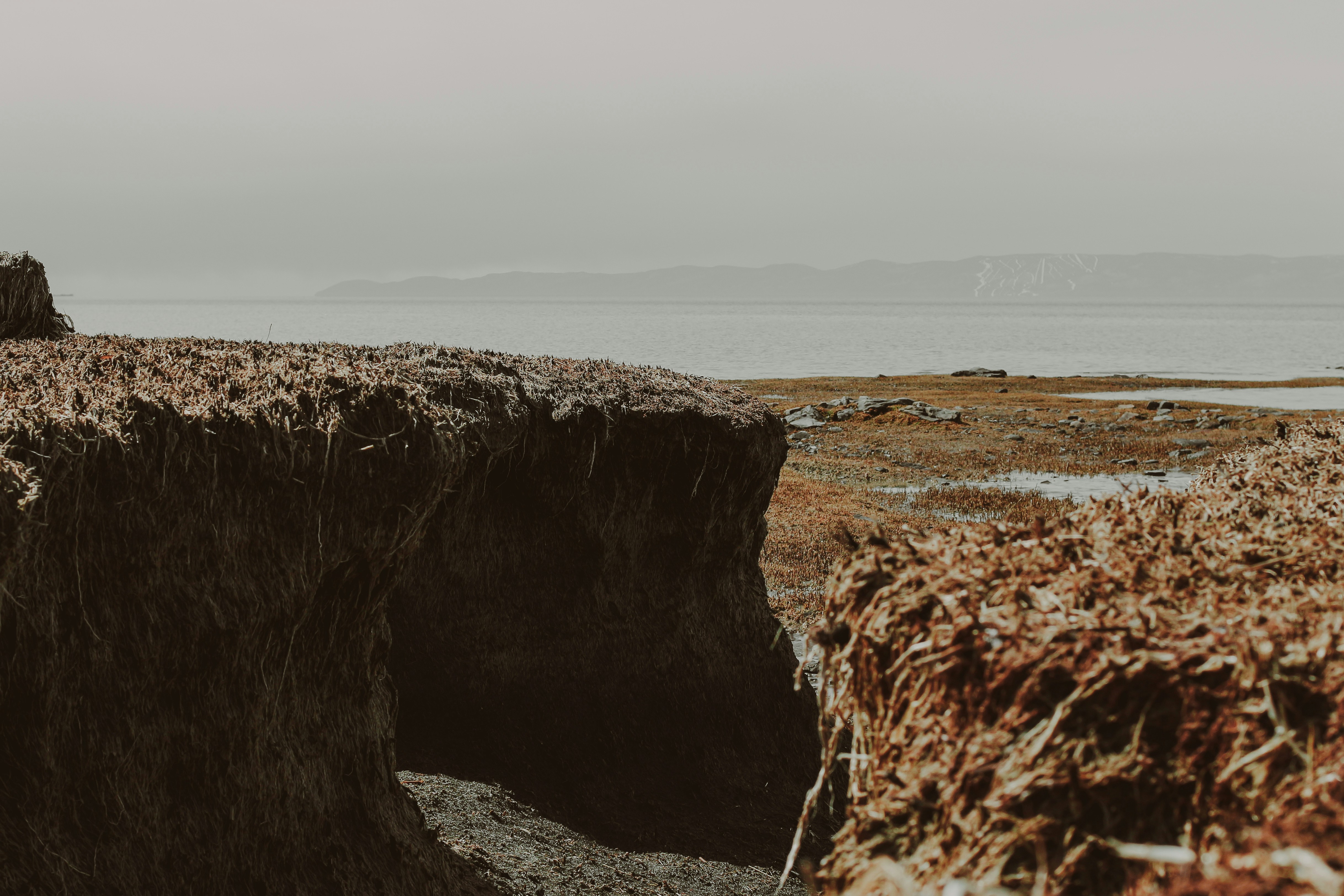 A man standing on top of a cliff next to a body of water photo – Free ...