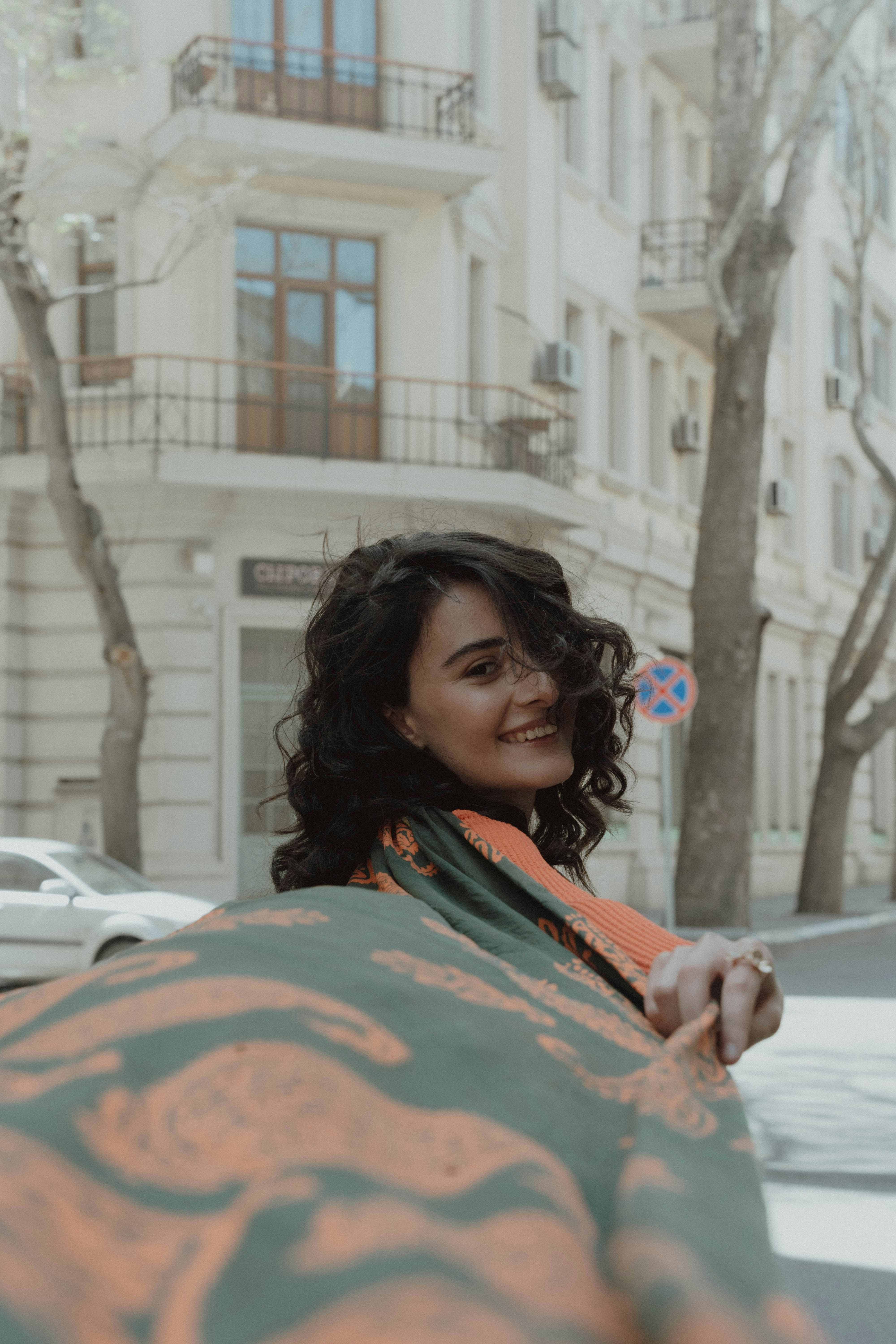 Sunlit City Portrait: A joyful smile framed by a patterned scarf along a classic street