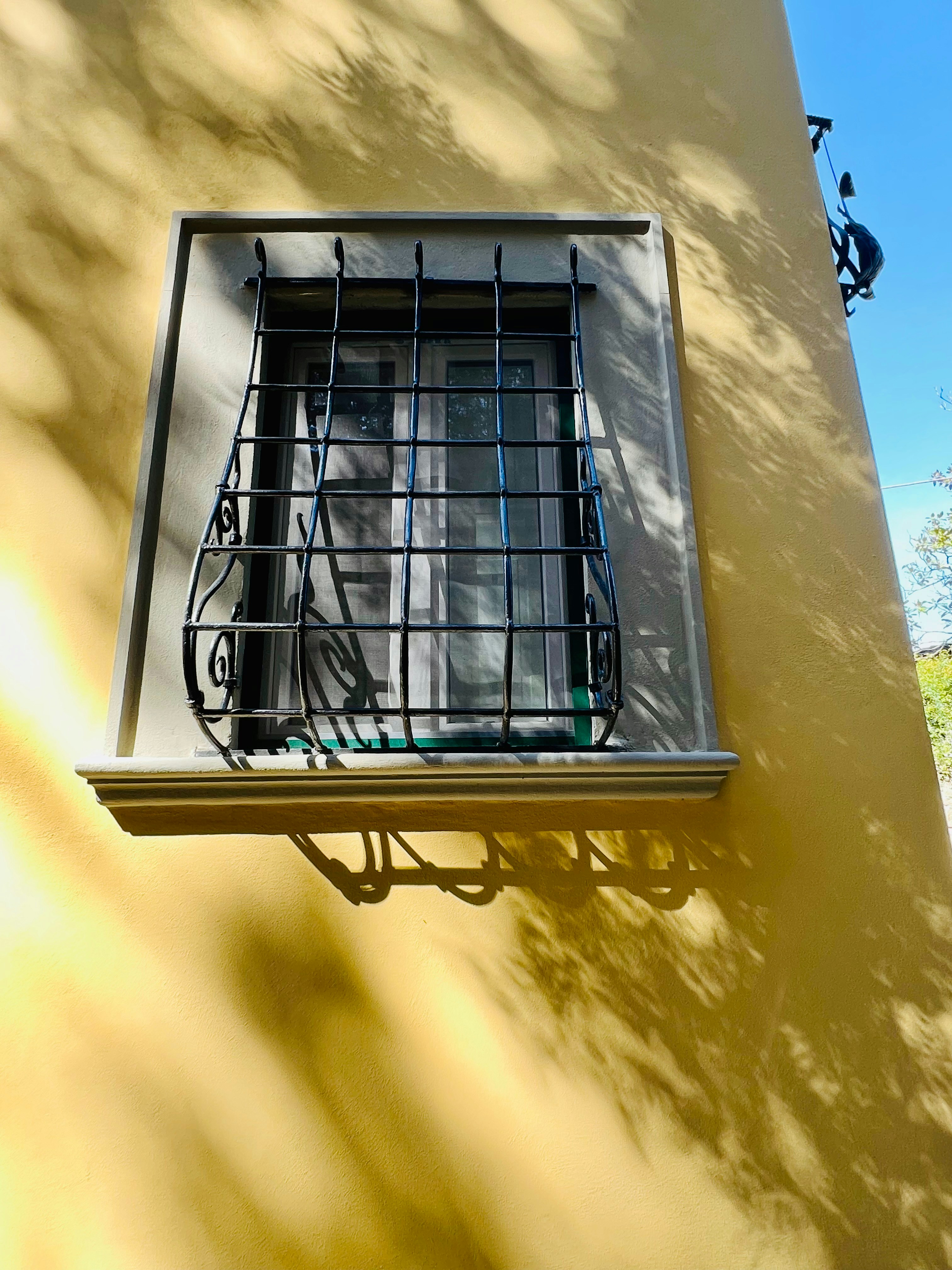 Barred Window on a Sunlit Yellow Facade: Shadow Play Across Warm Stucco