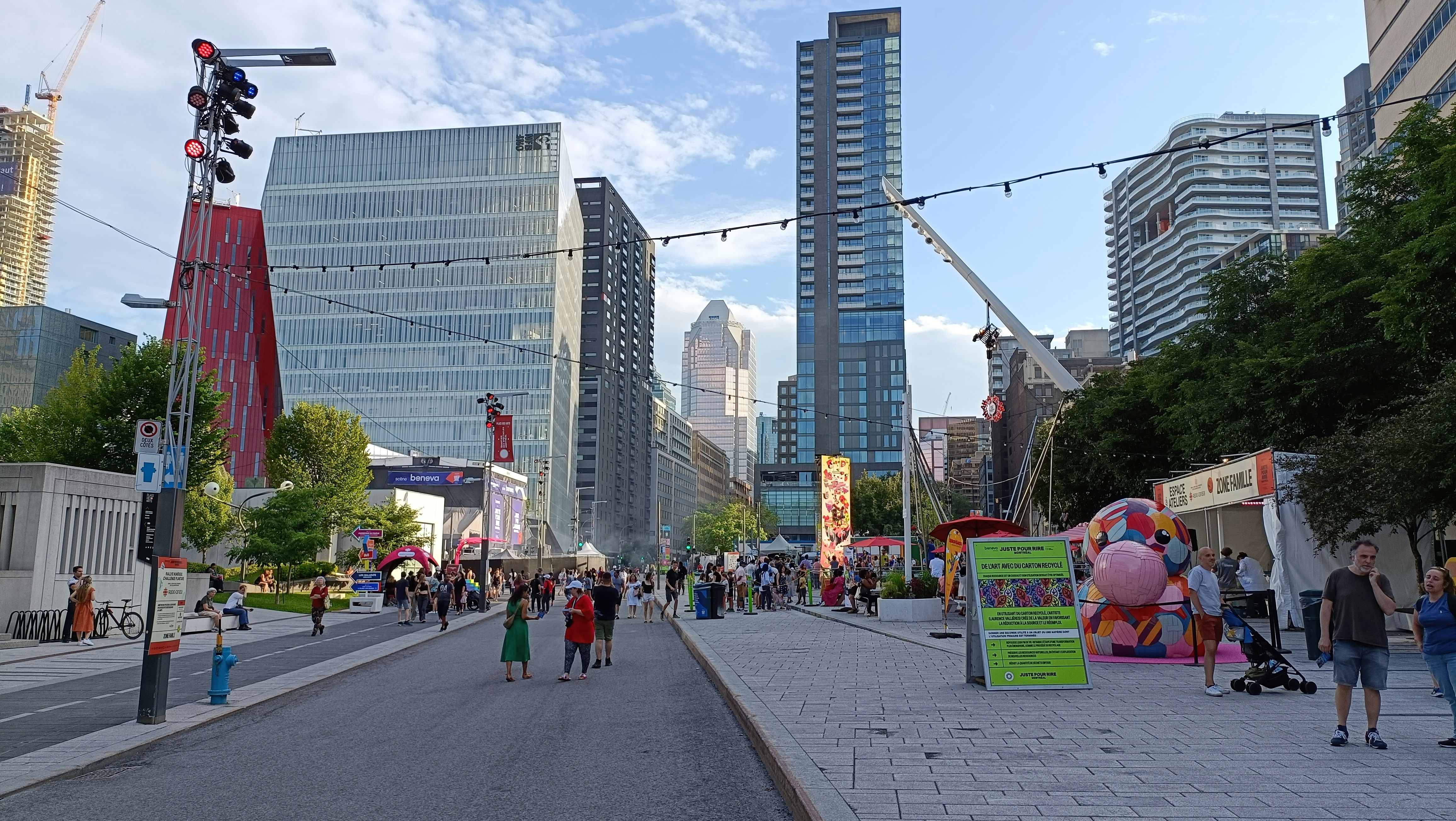 Busy city street festival with colorful stalls and balloons along a pedestrian corridor under modern skyscrapers.