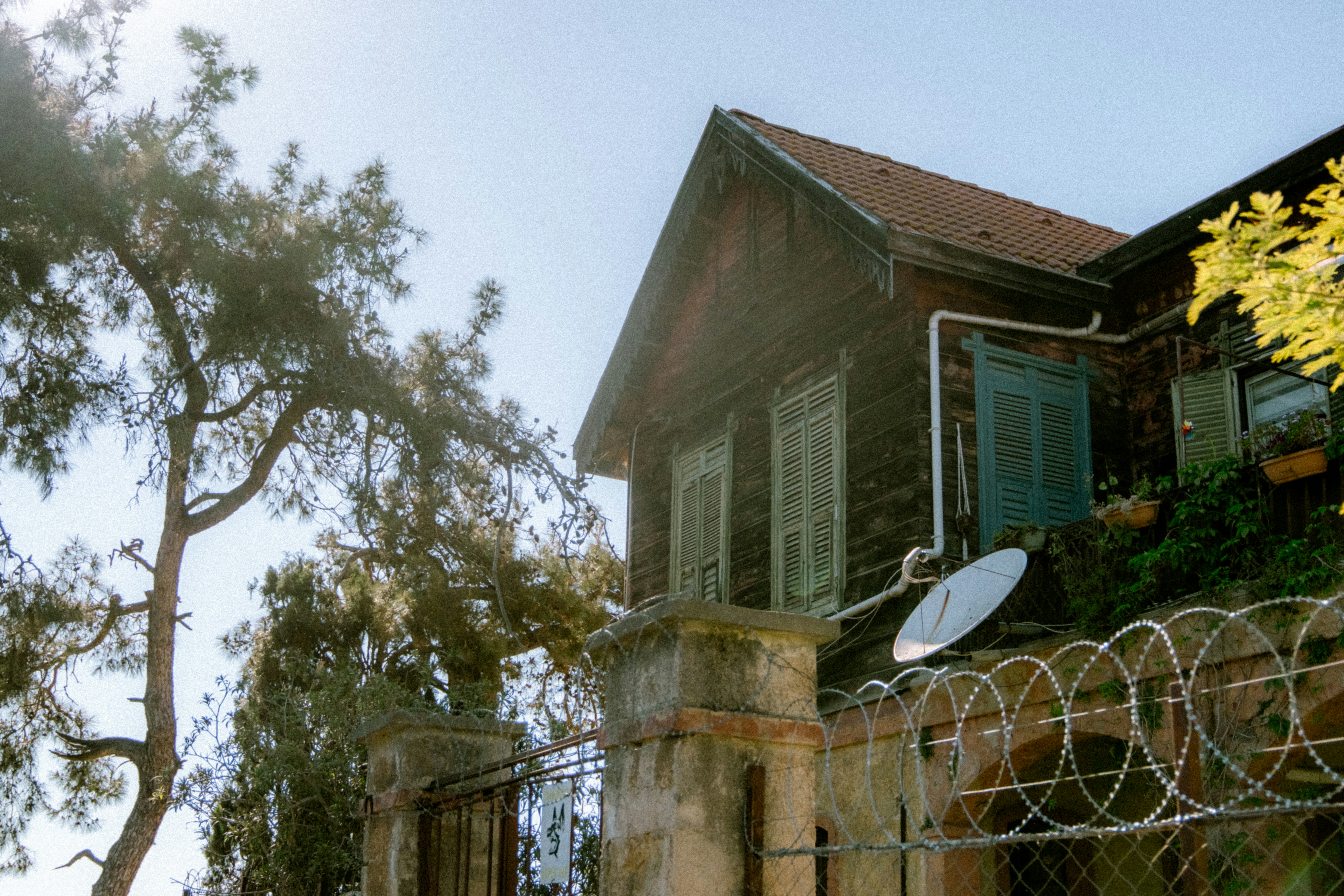 Satellite Dish Hangs Over Barbed-Wire Fence at Drowsy Roofline