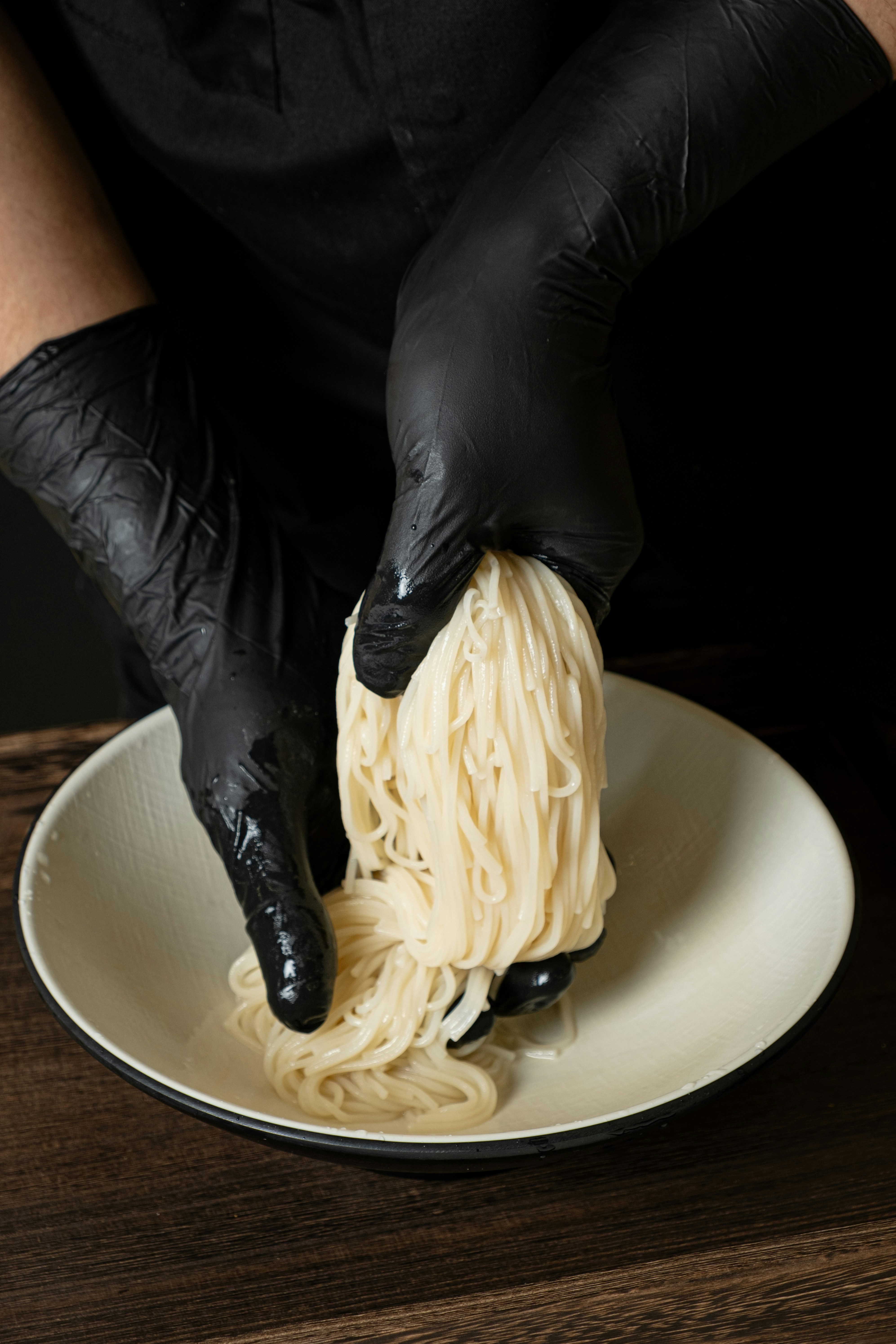 Hands in black gloves skillfully lifting freshly cooked noodles from a bowl, showcasing the art of pasta preparation.