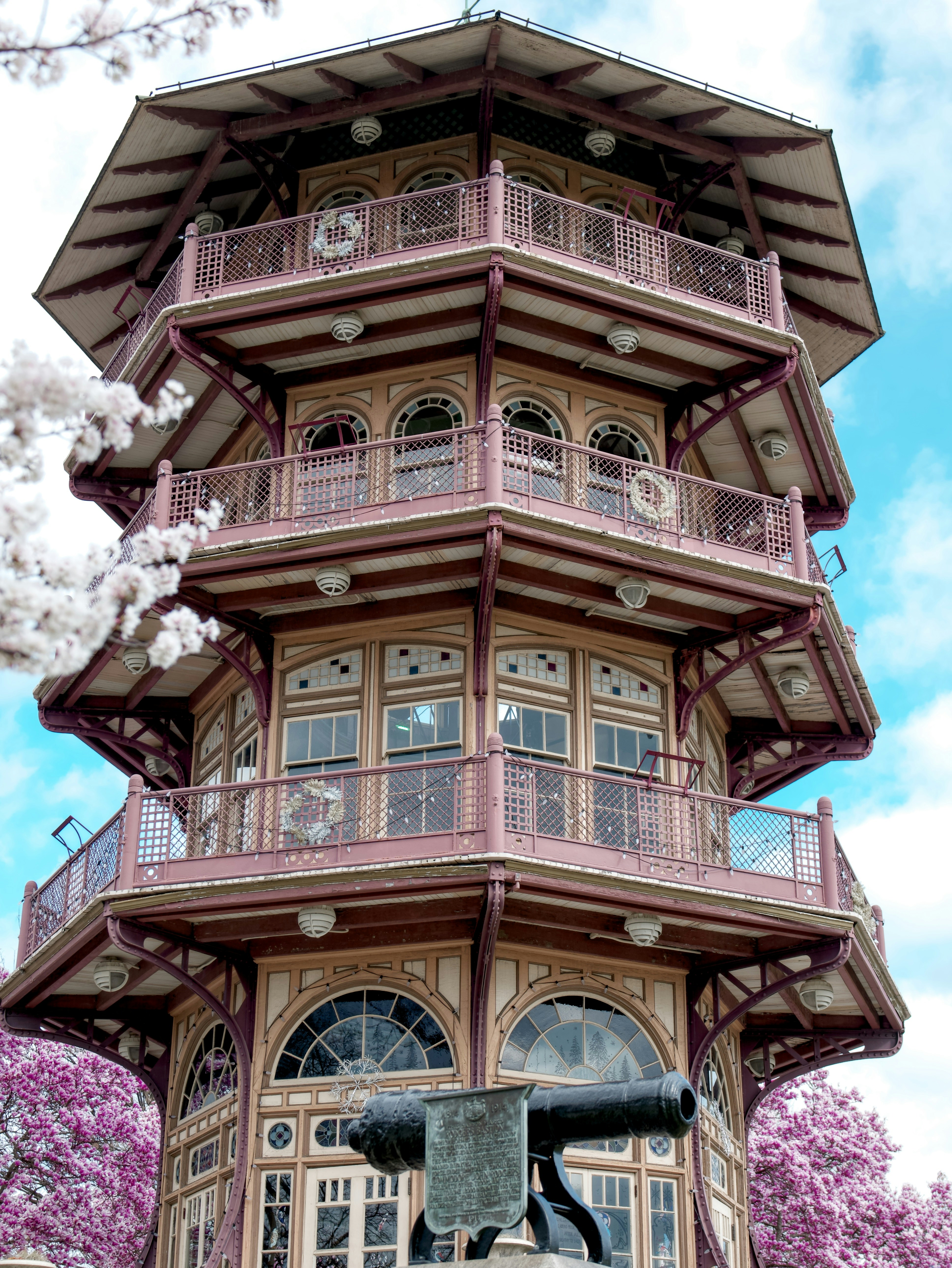 Multi-tiered pagoda with intricate wooden details surrounded by vibrant cherry blossoms and a bright blue sky.