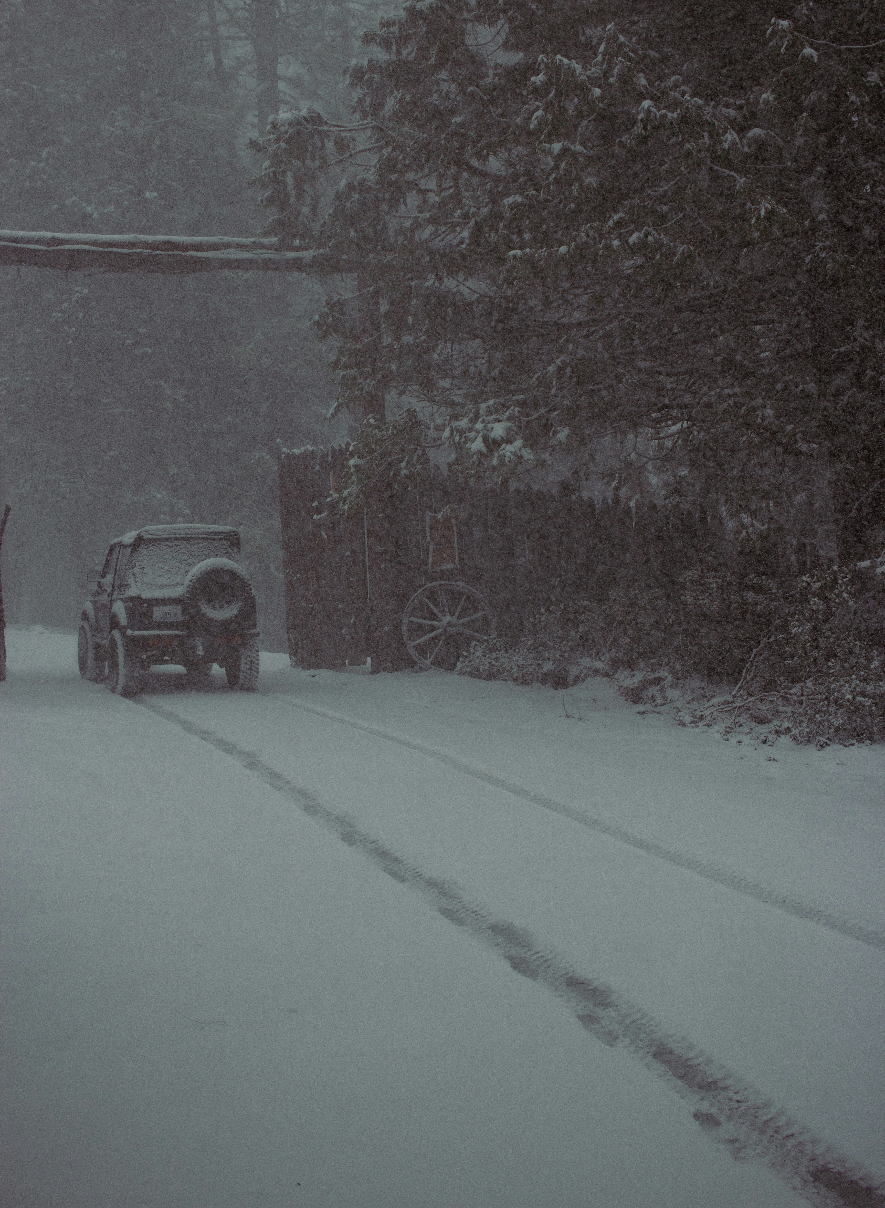 A rugged vehicle rests on a snow-covered path, surrounded by a tranquil winter landscape shrouded in soft falling snowflakes.