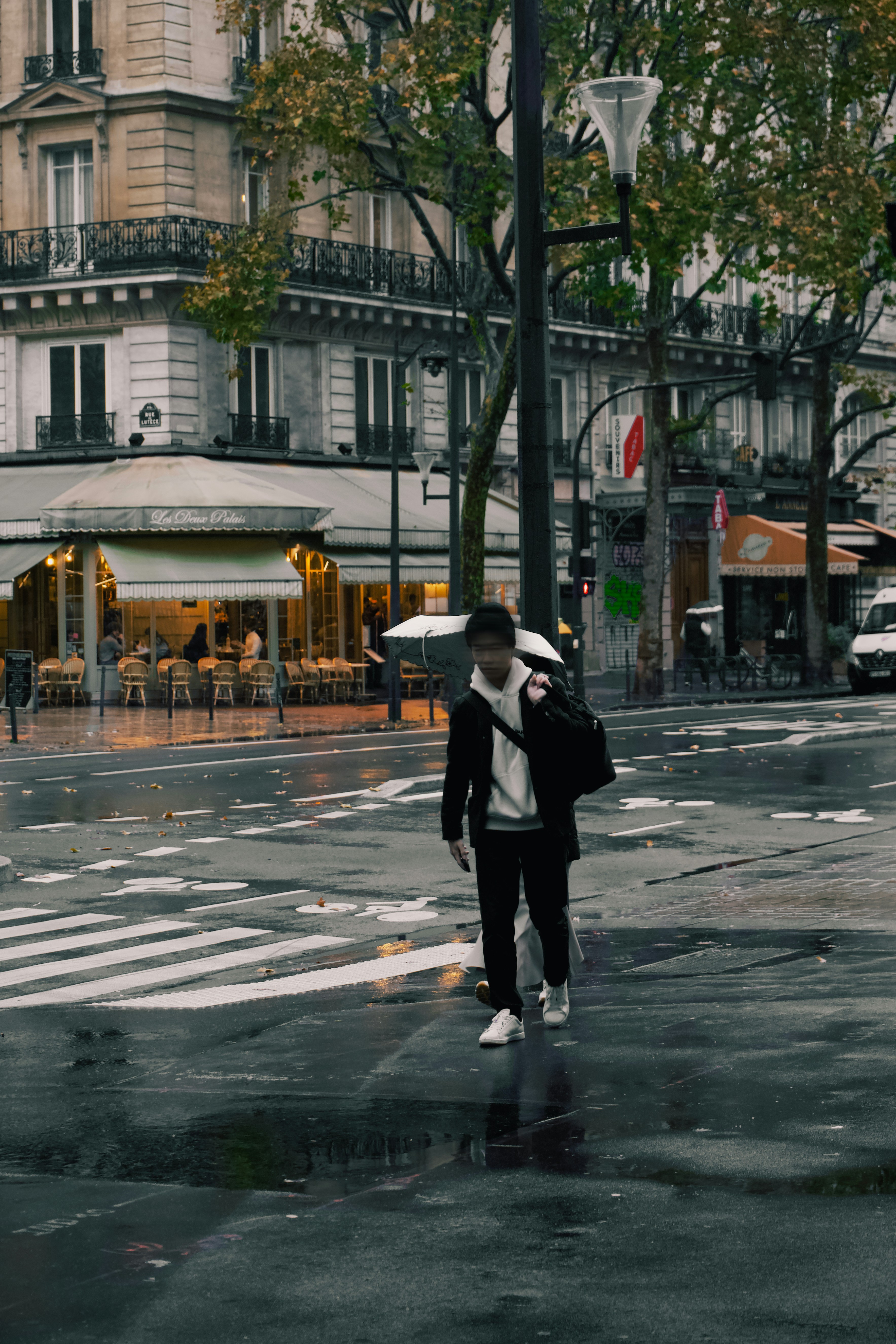 Crossing Rain: Pedestrian in the Warm Glow of a Parisian Café