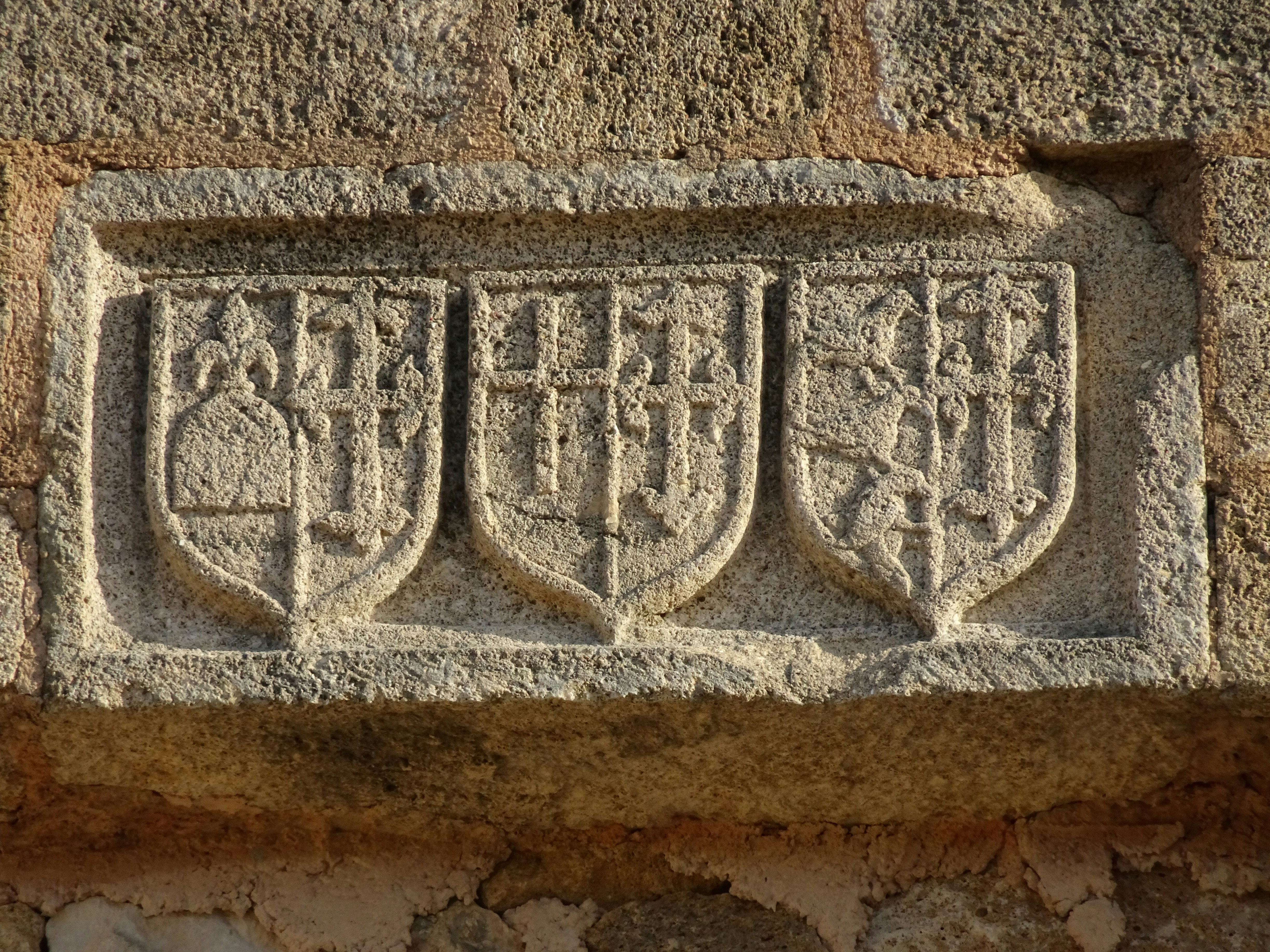Stone relief carving featuring a row of three heraldic shields set in weathered masonry.