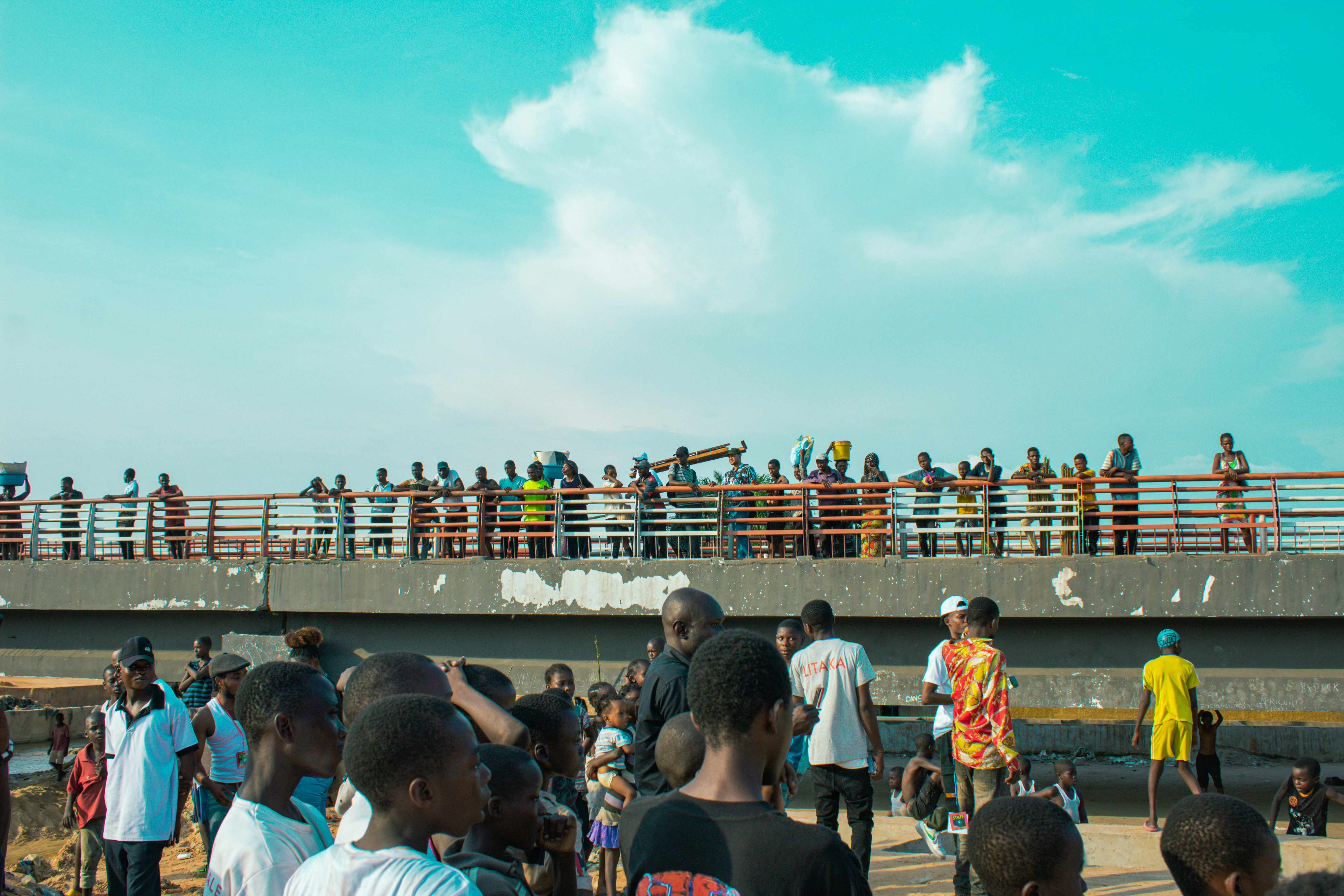Crowd gathered on a bridge under a vibrant blue sky with scattered white clouds.