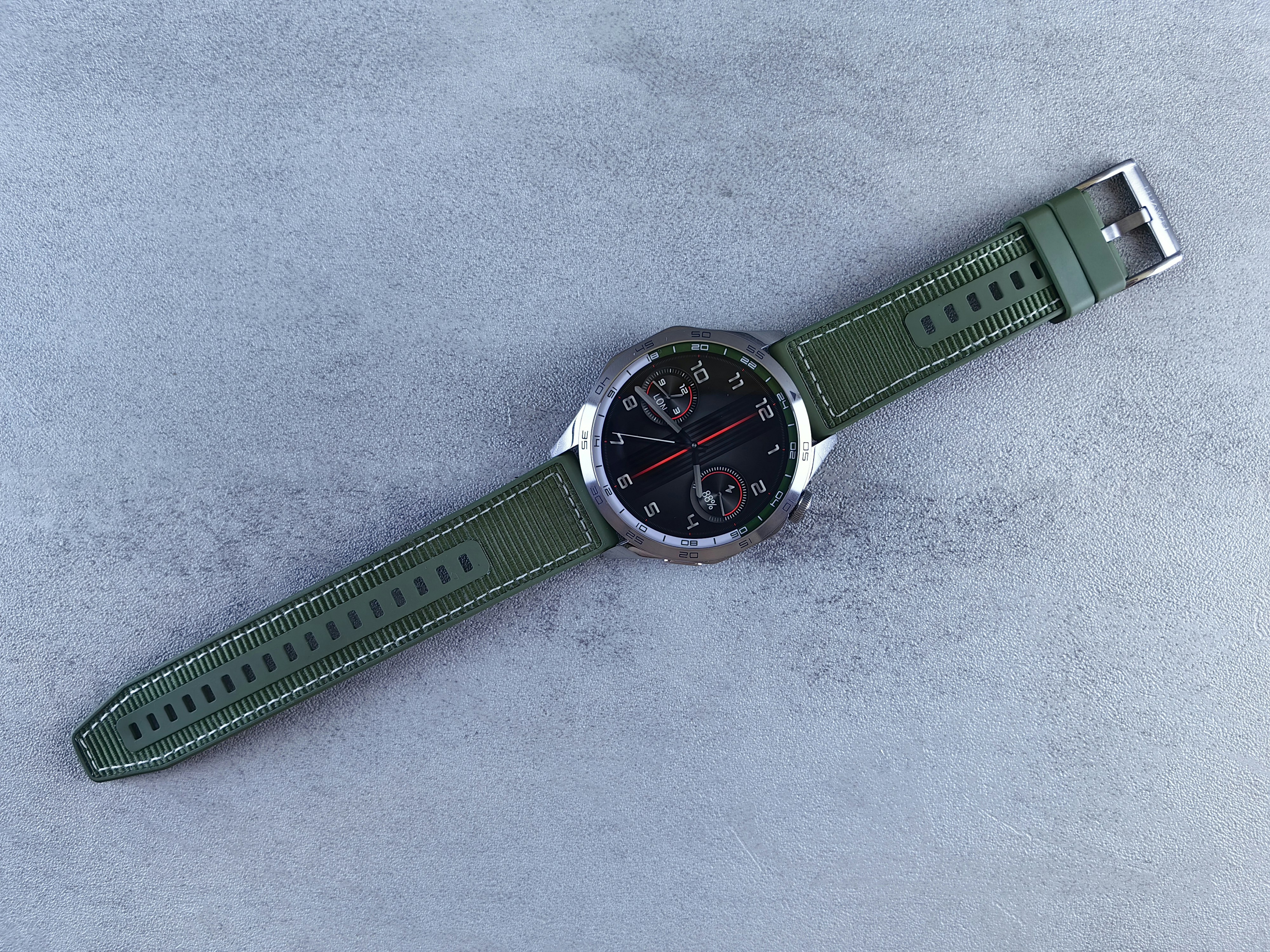 Green-strapped wristwatch rests diagonally on a matte gray surface, its dial and metallic bezel crisply rendered in this photograph for a clean, modern portrait.