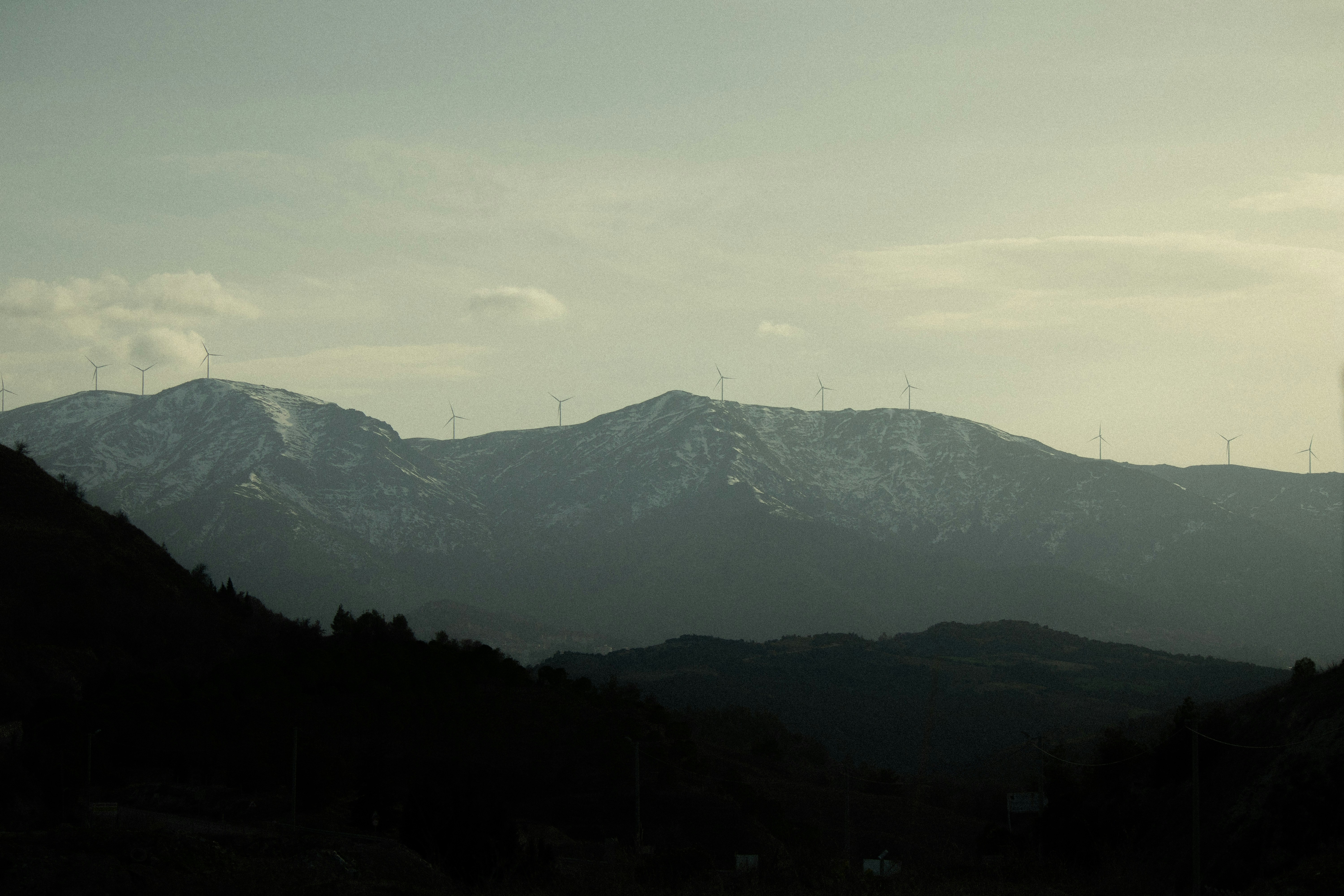 A view of a mountain range with wind mills in the distance photo – Free ...