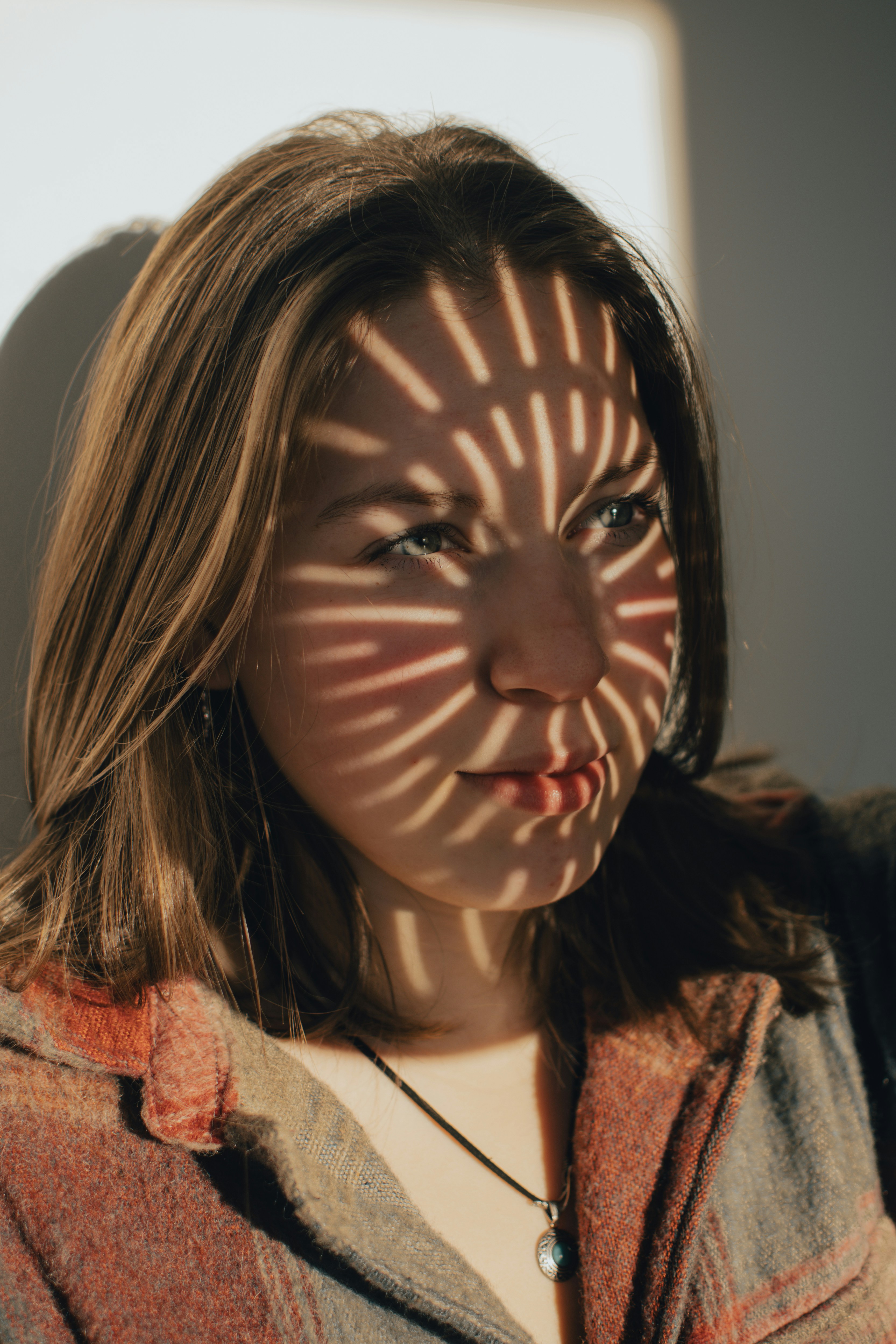 Portrait of a woman with a striped shadow pattern across her face, creating geometric lines and warm mood.