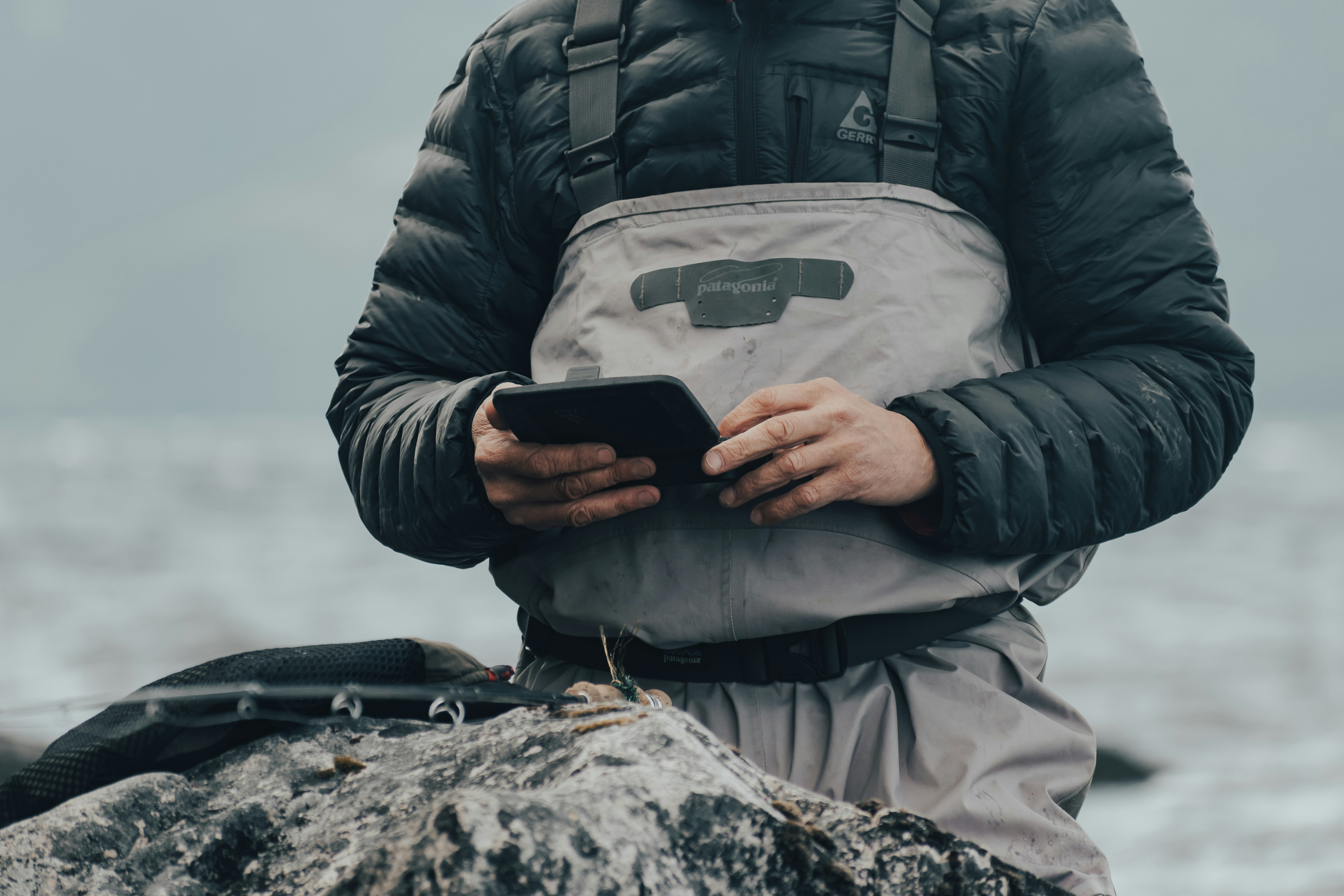 Portrait in a rugged shoreline jacket: hands and device as focal point