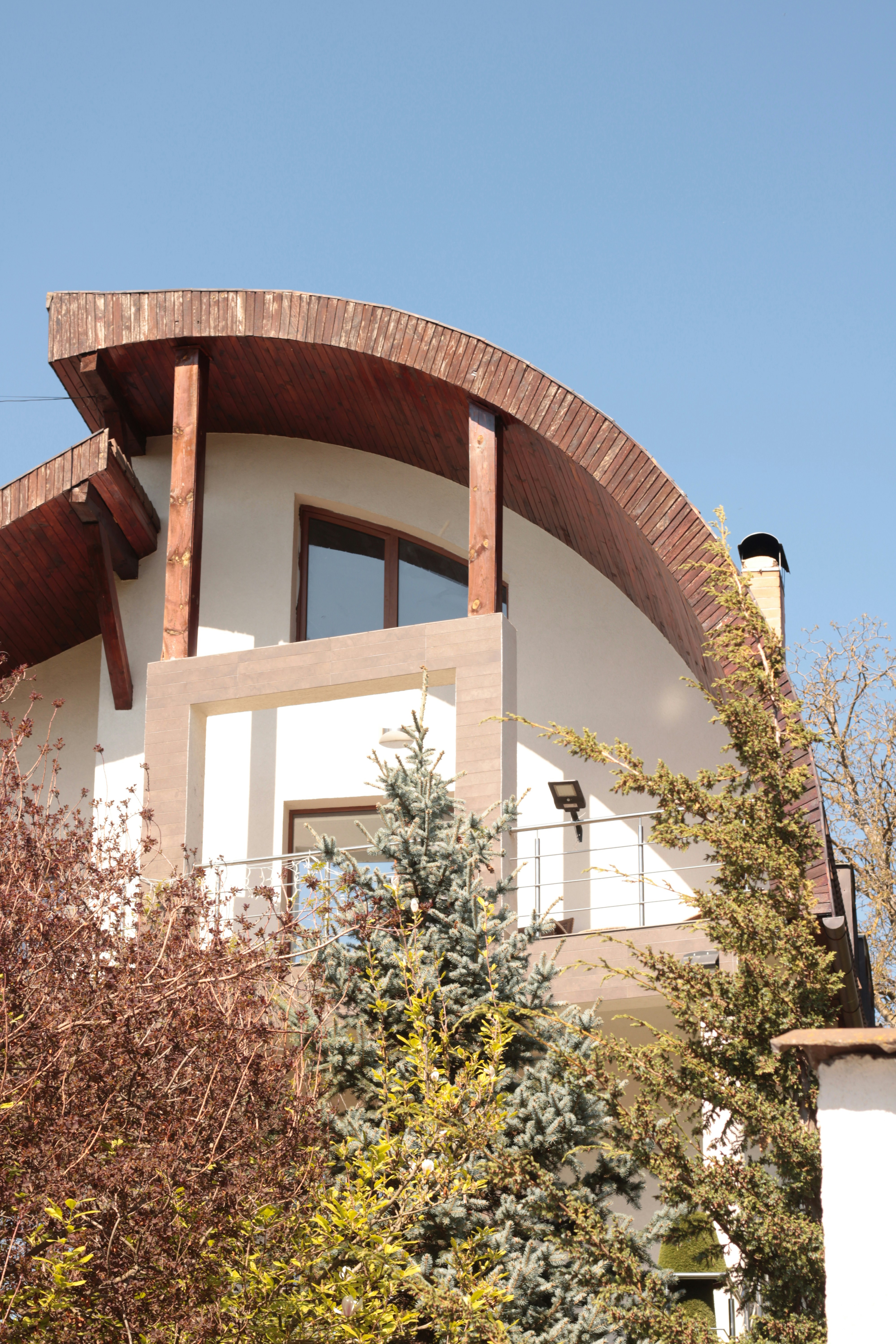 Curved Timber Roof Over White Facade: A Modern Villa Framed by Autumn Foliage