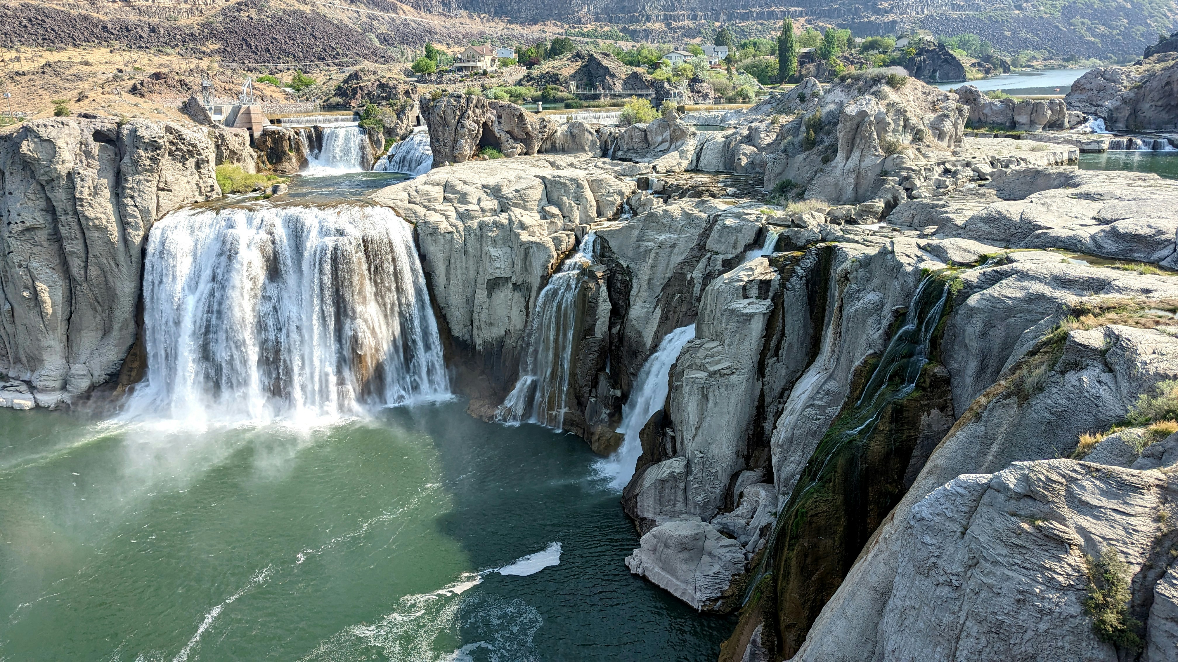 A man standing atop a large waterfall, surrounded by rugged cliffs and cascading water.