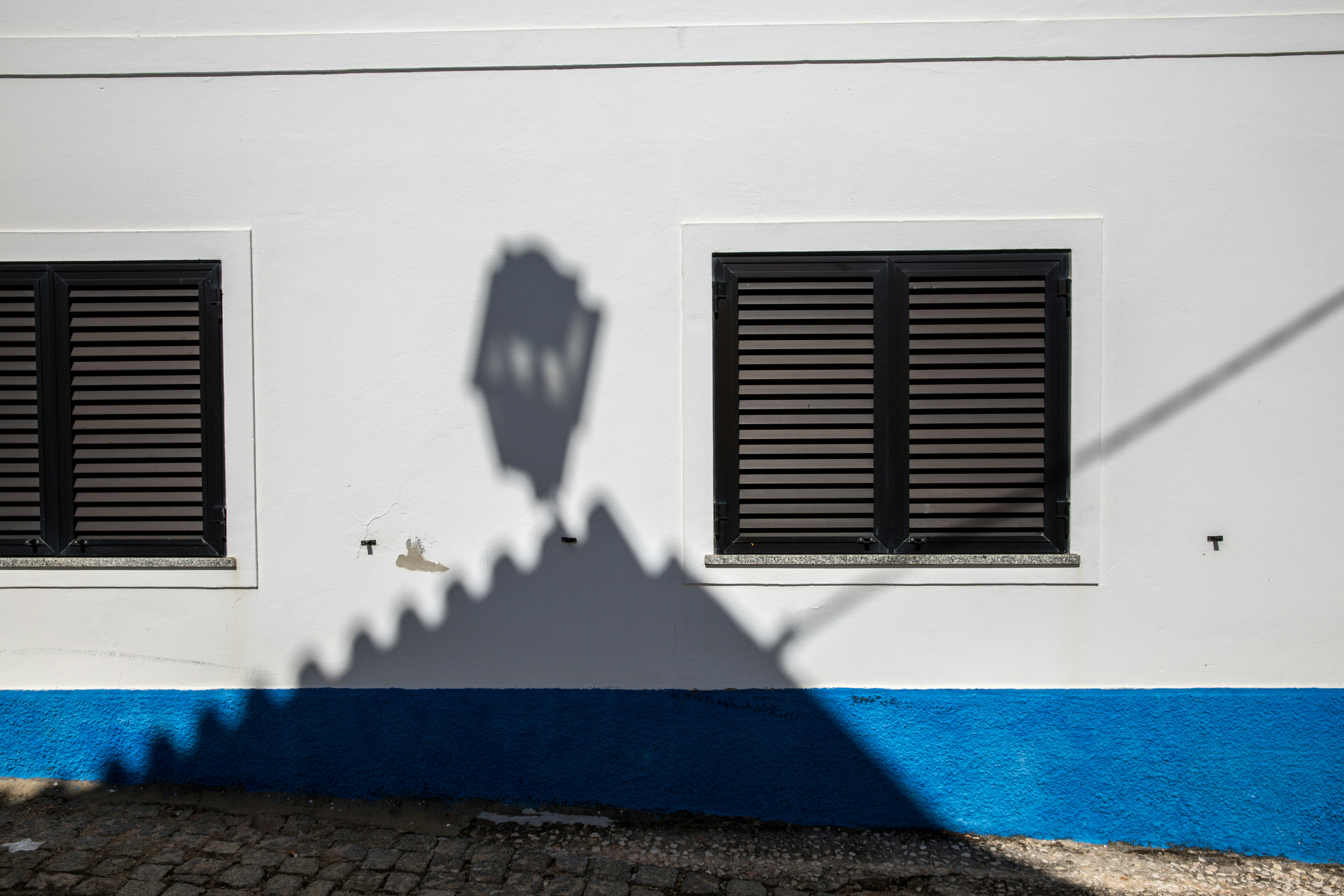 White and blue facade, street of a Portuguese village, long shadow of a street lamp