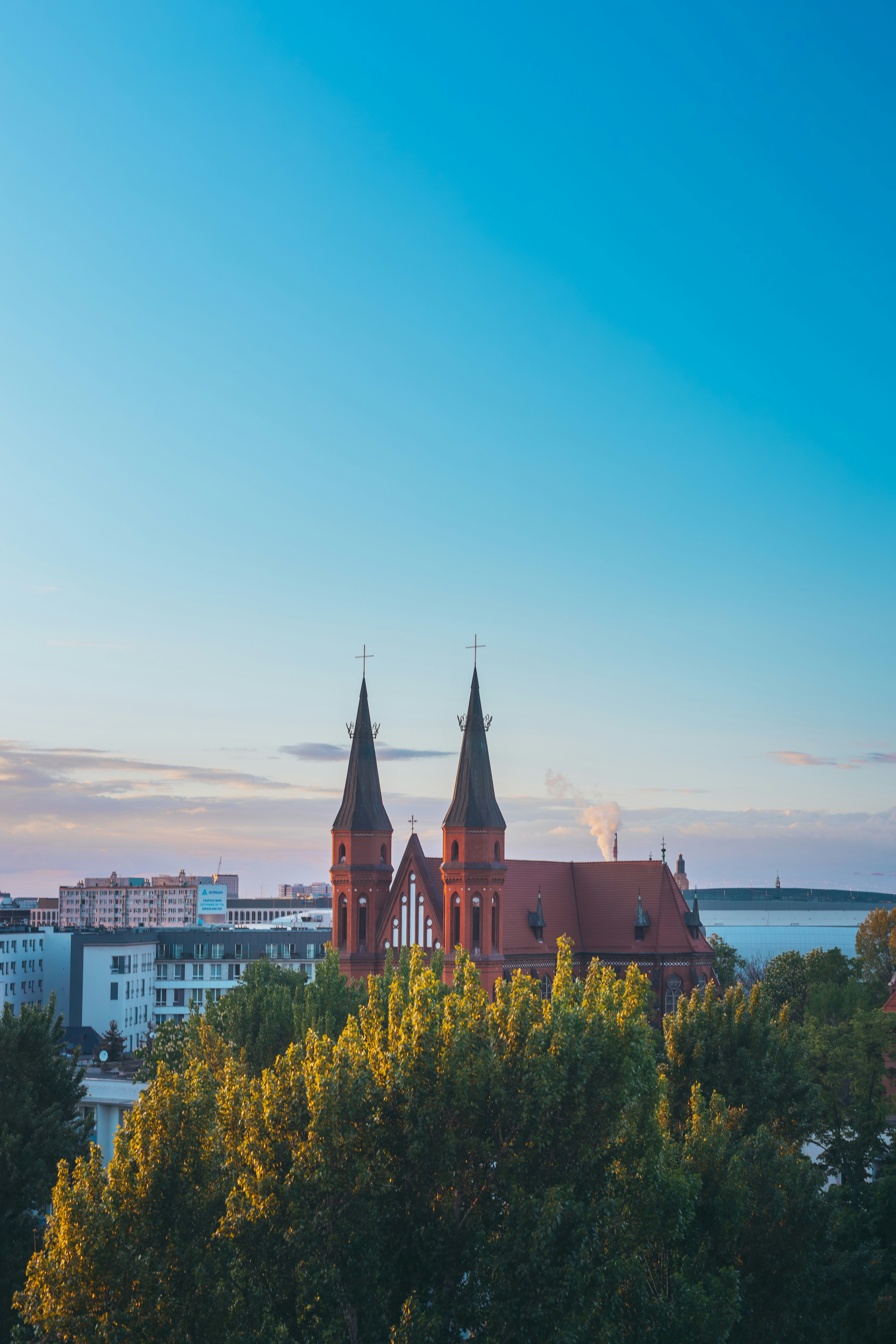 Historic church featuring twin spires, framed by lush greenery and a pastel sky at dusk.