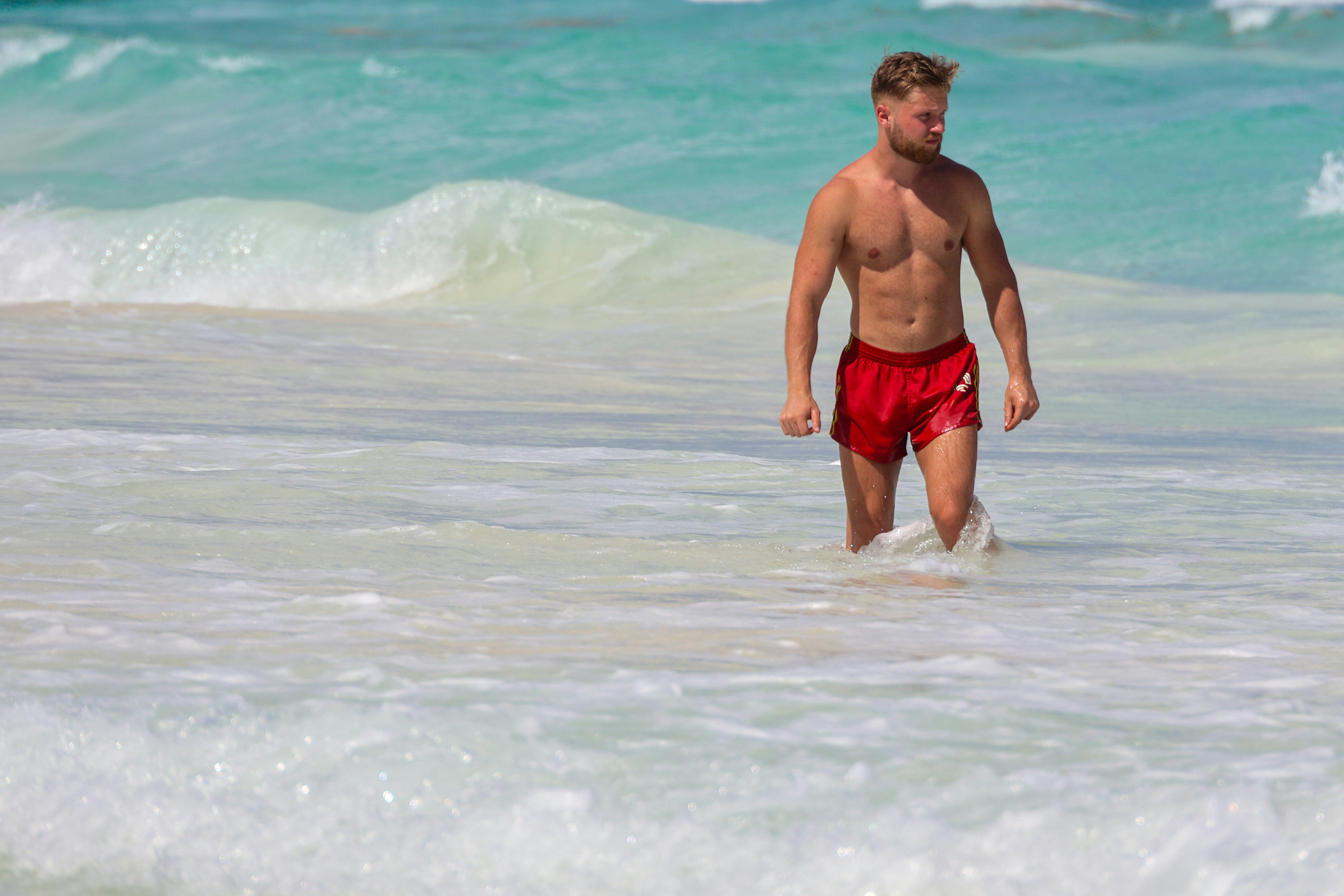A man in red swim trunks walking into the ocean photo – Free Tulum ...