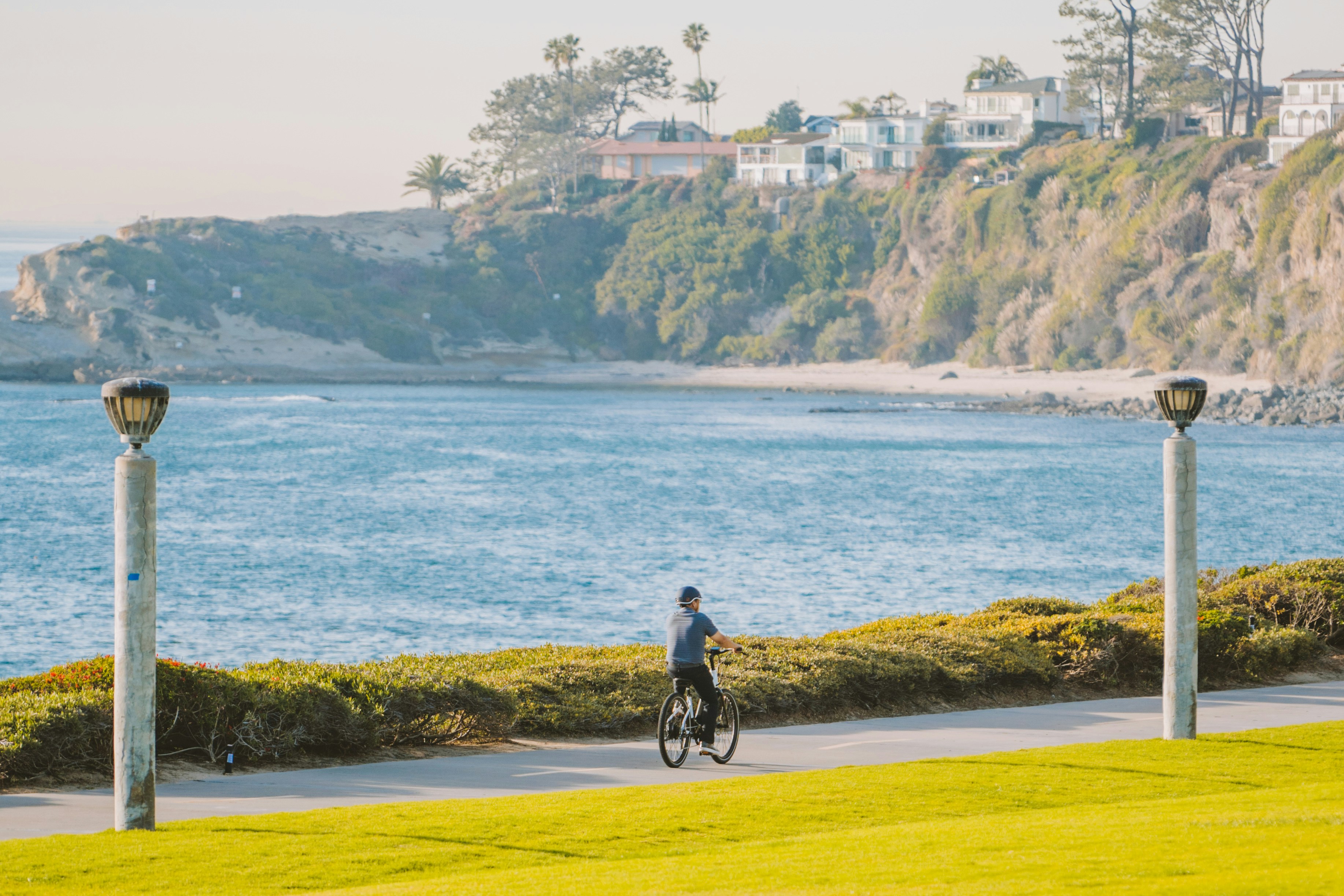 A man riding a bike down a sidewalk next to a body of water photo ...