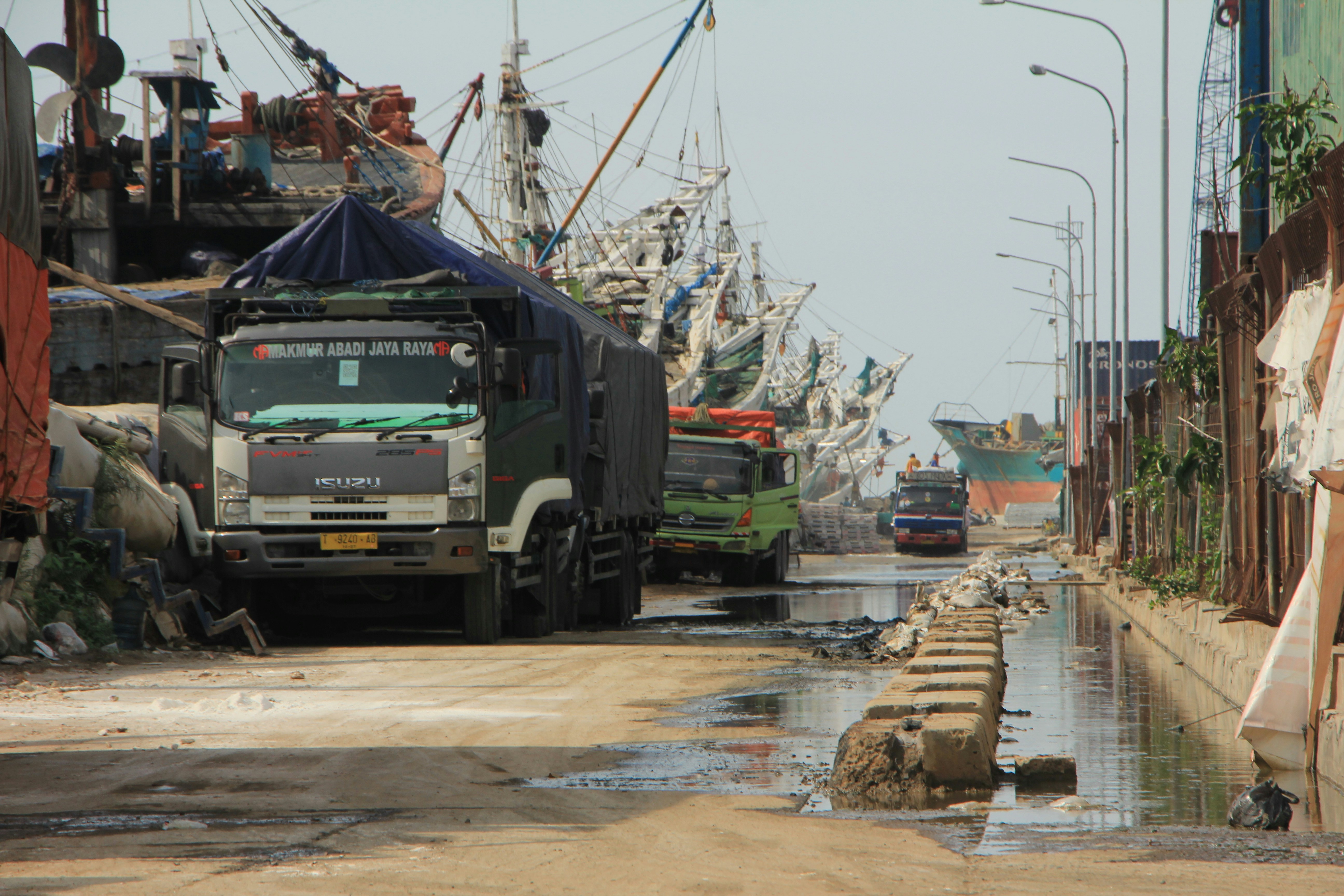 Trucks parked alongside traditional wooden cargo boats at Sunda Kelapa Harbour in Jakarta.