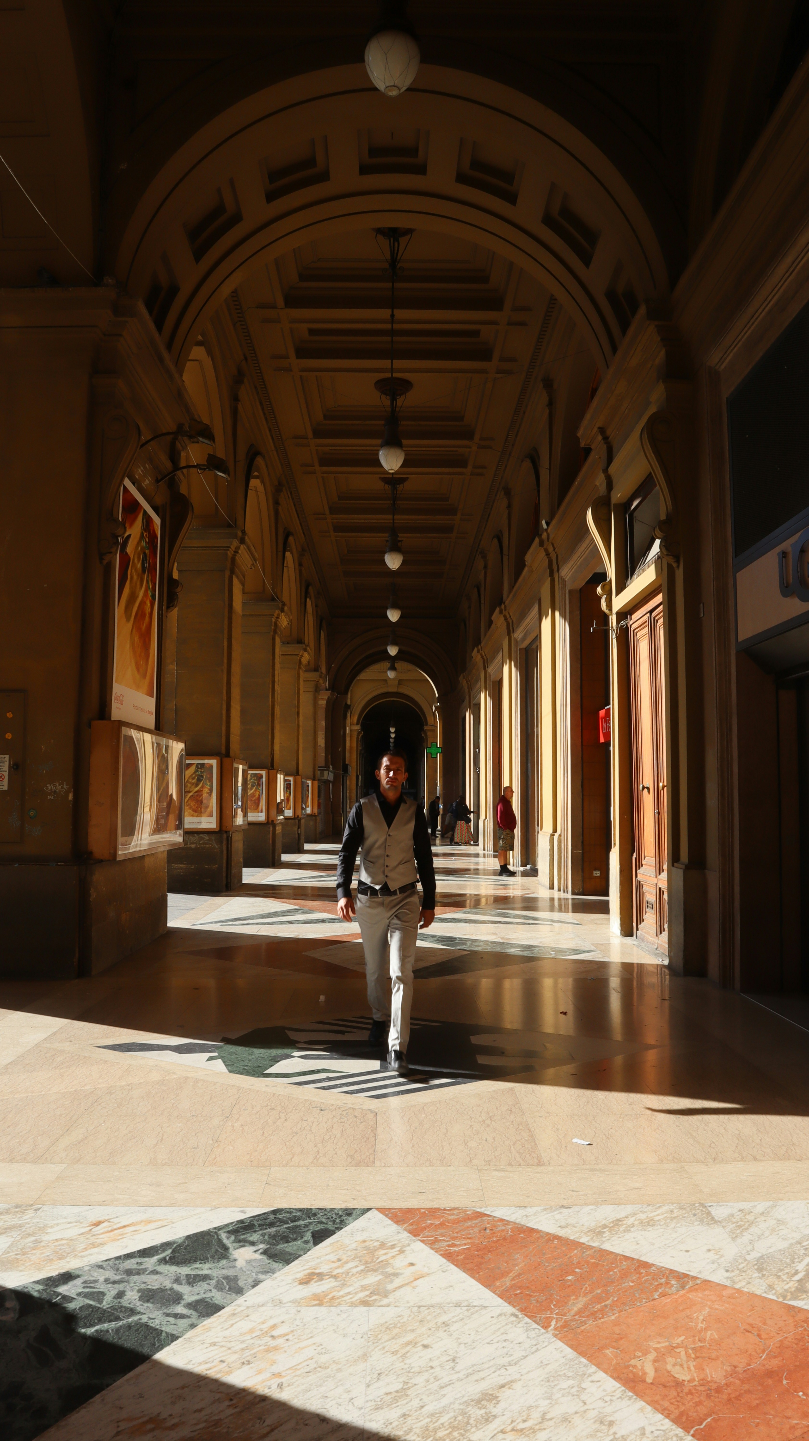 Arcade of Echoes: A lone figure walks through sunlit arches