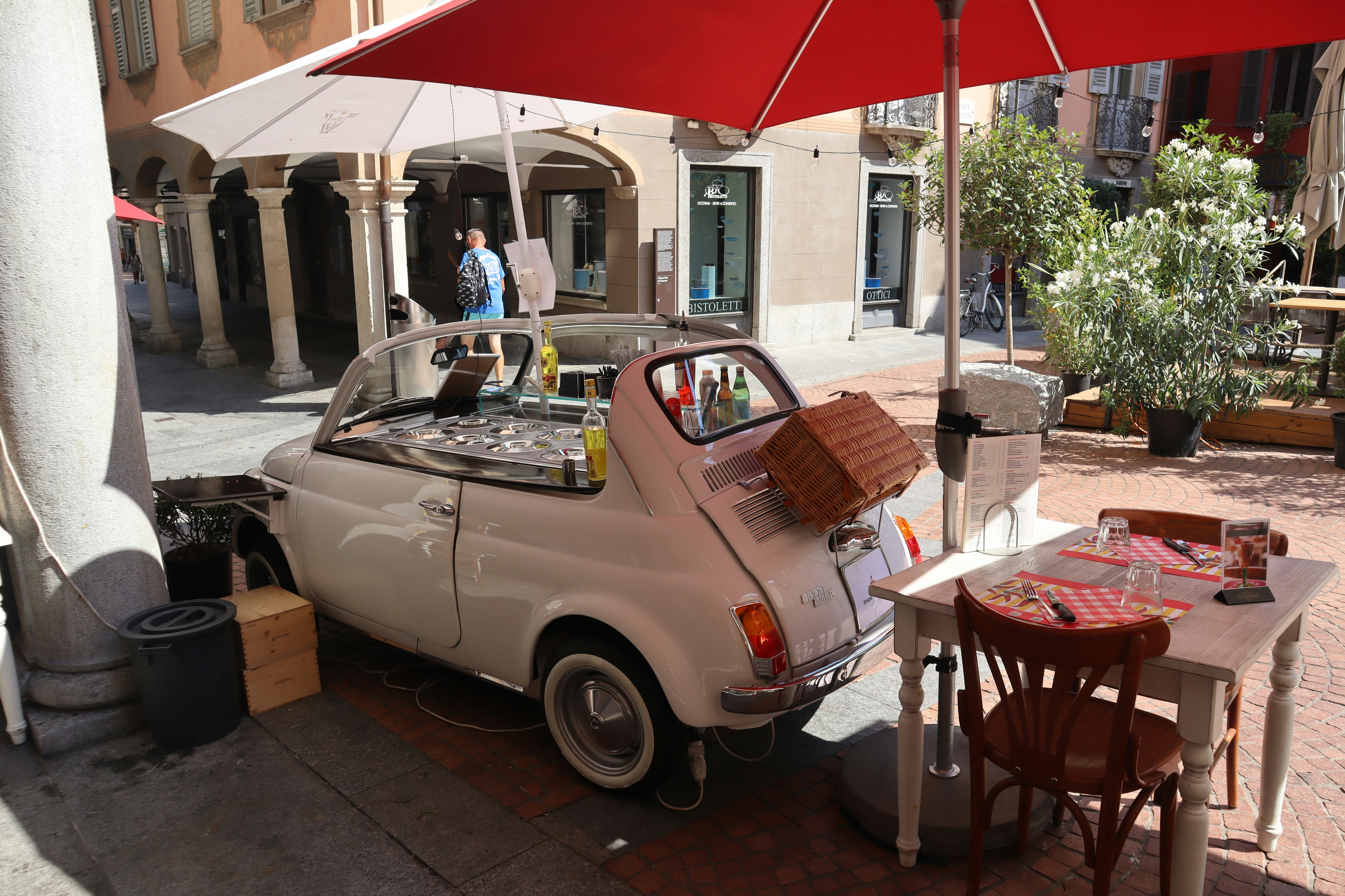 Sunlit European Street Café with Vintage Car under Red Canopy