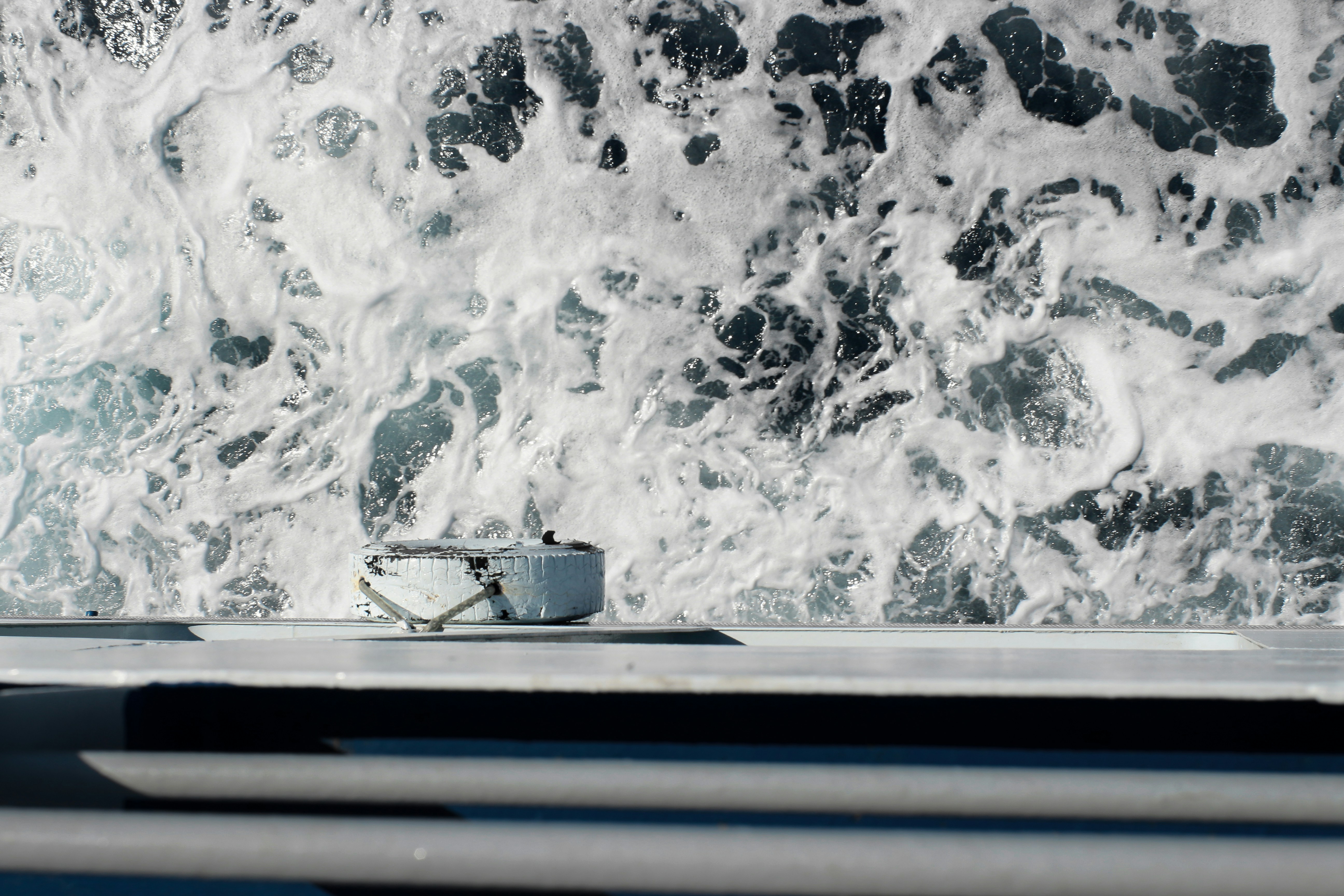 Foamy ocean waves crashing against a ship's deck, with a circular white object resting on the surface. The scene captures the dynamic interaction between water and vessel.