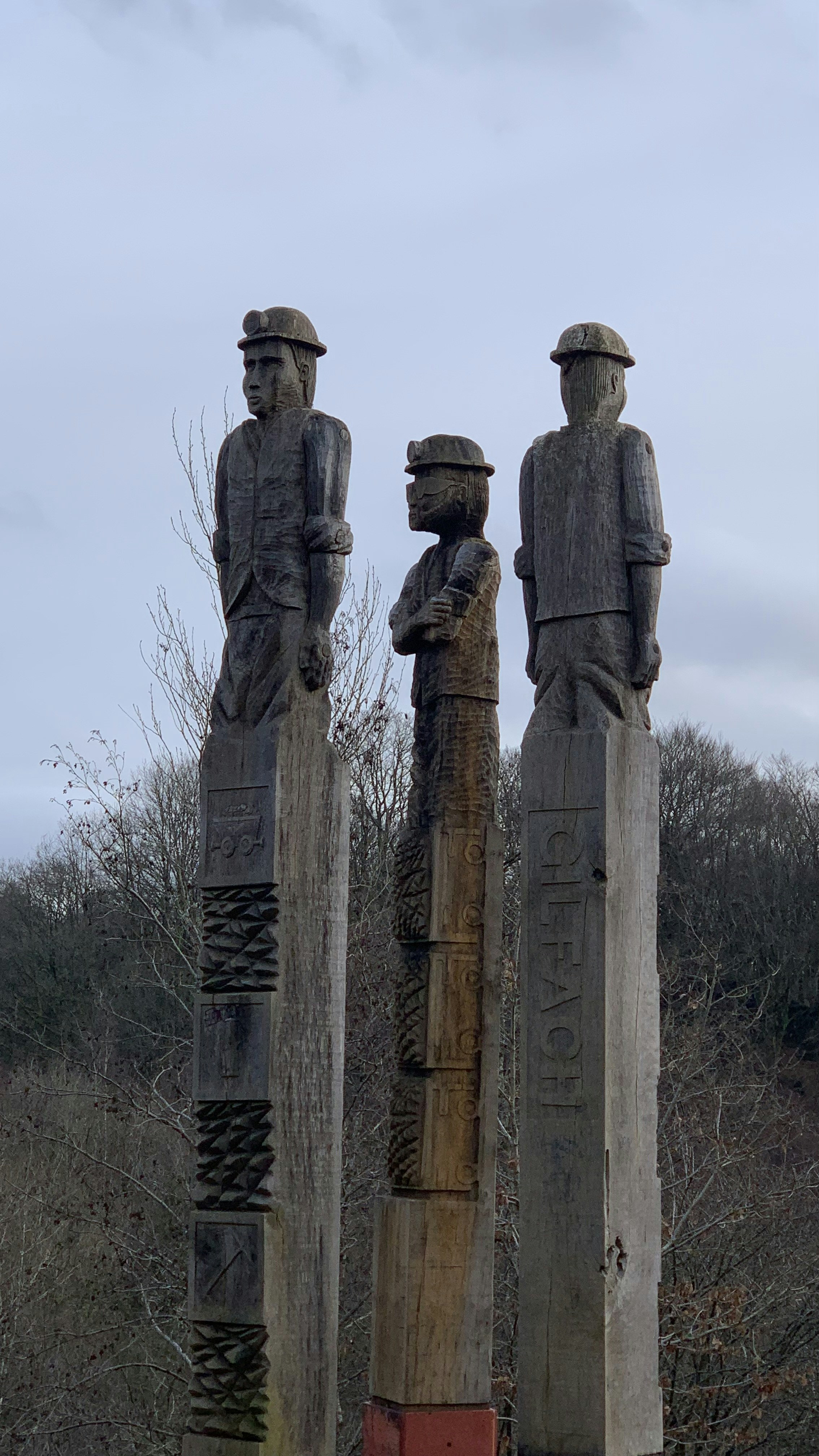 Three carved totems rise above bare trees under a pale sky