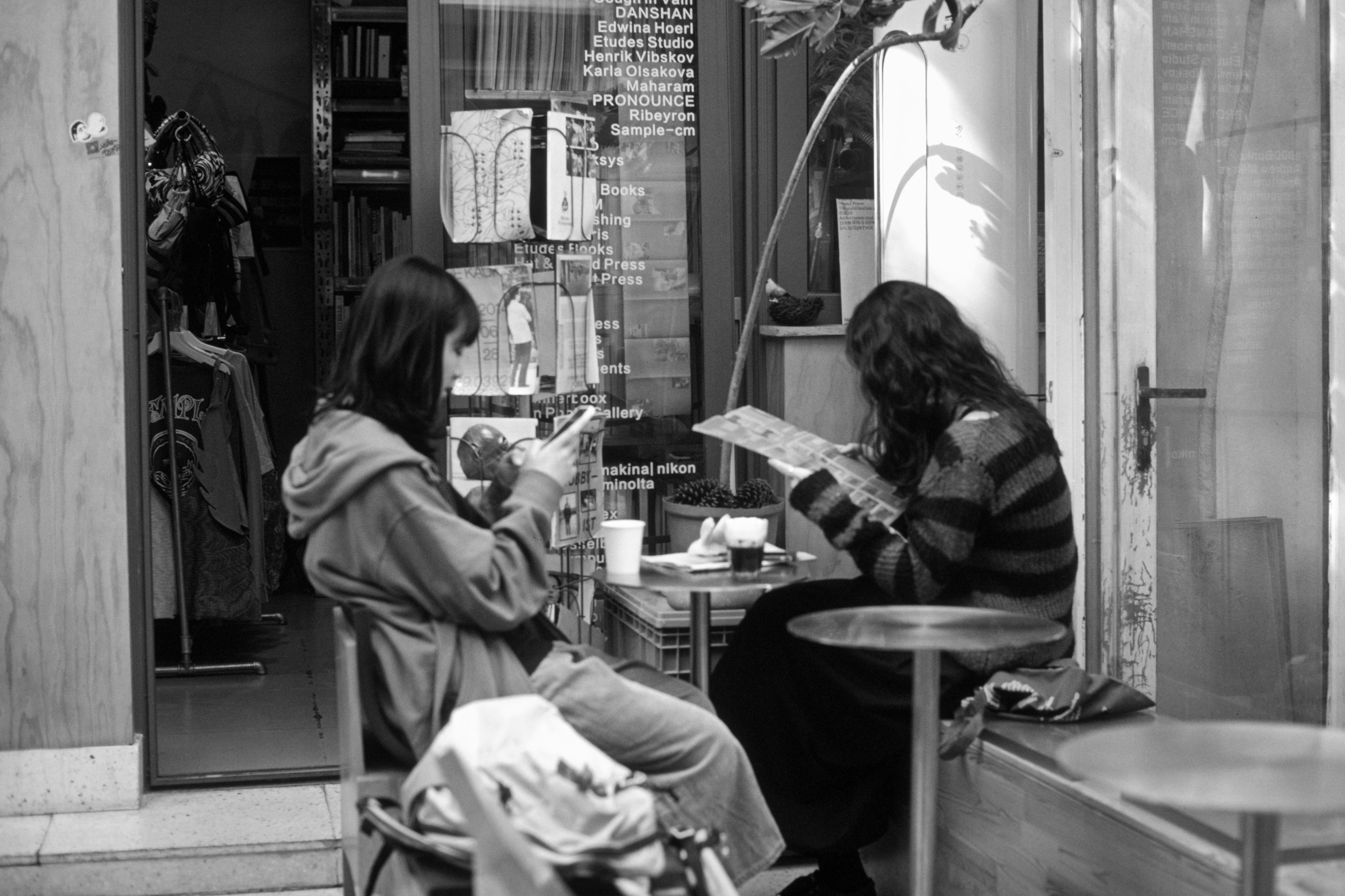 In the tranquility of the coffee shop, individuals are each busily engaged in their own affairs. | two women sitting at a table in front of a store
