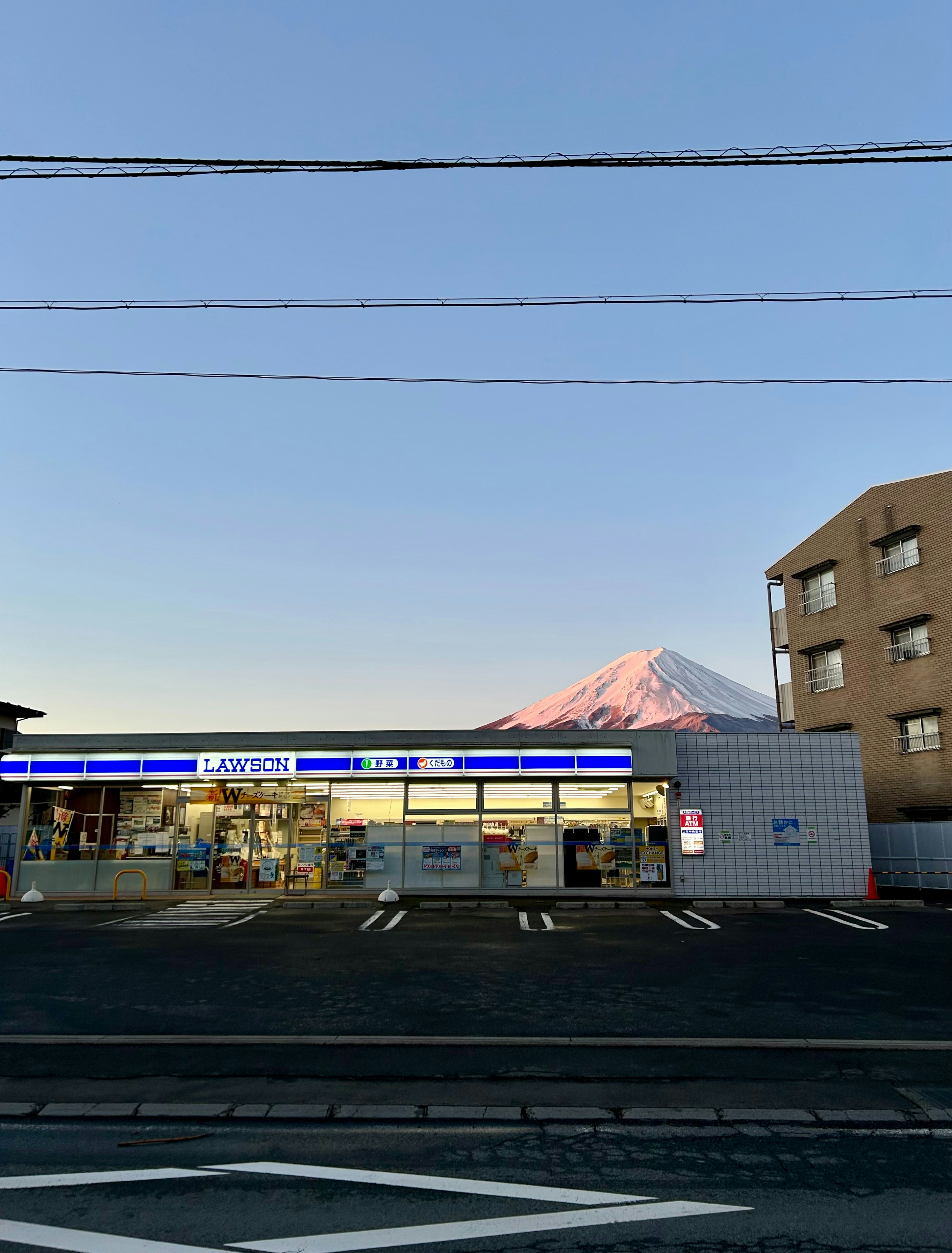 Photograph capturing pink-tinted Mount Fuji behind a Lawson convenience store at sunrise.