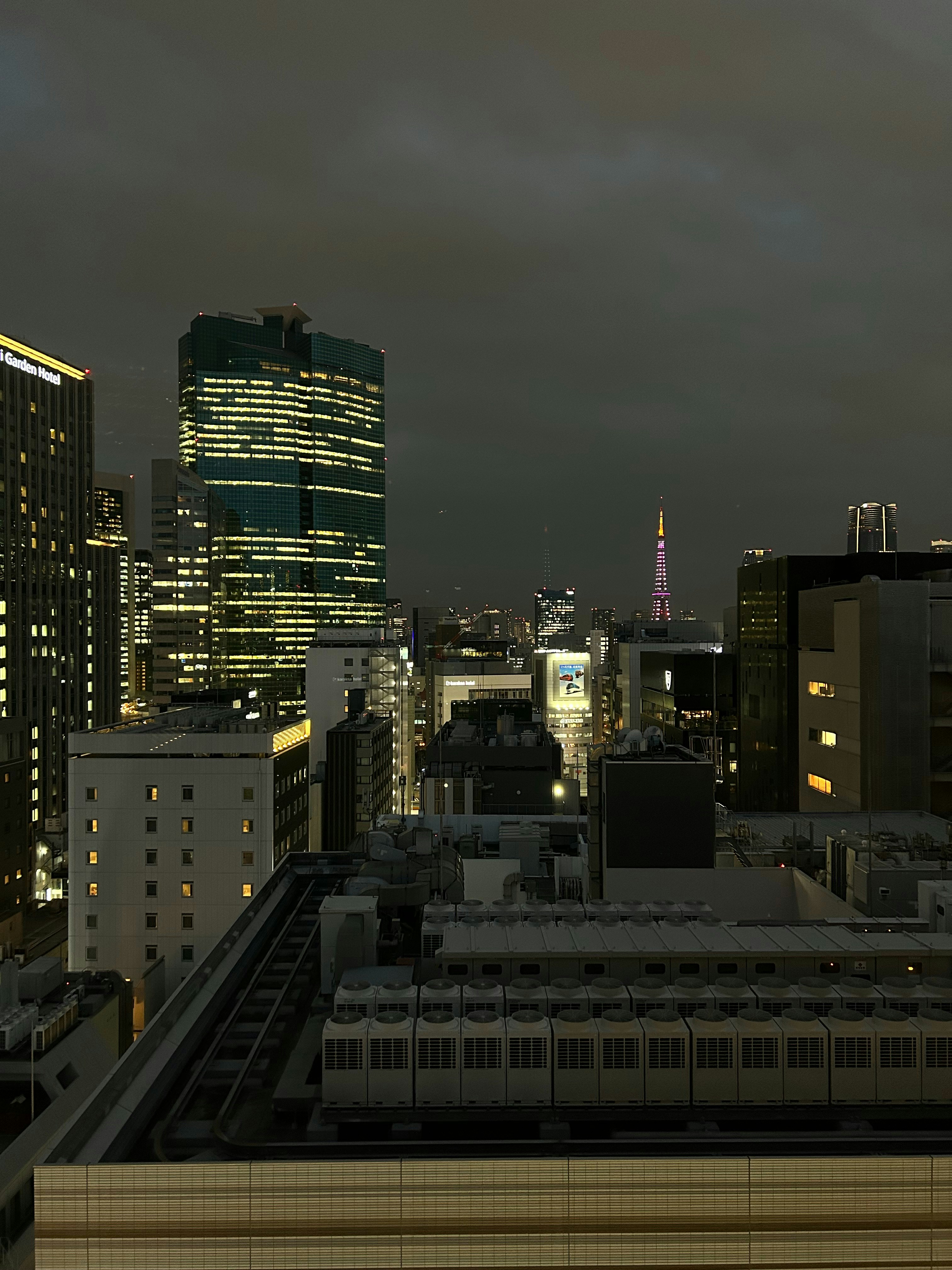 Nighttime cityscape photograph of a dense skyline with illuminated buildings and a purple-lit tower in the distance.