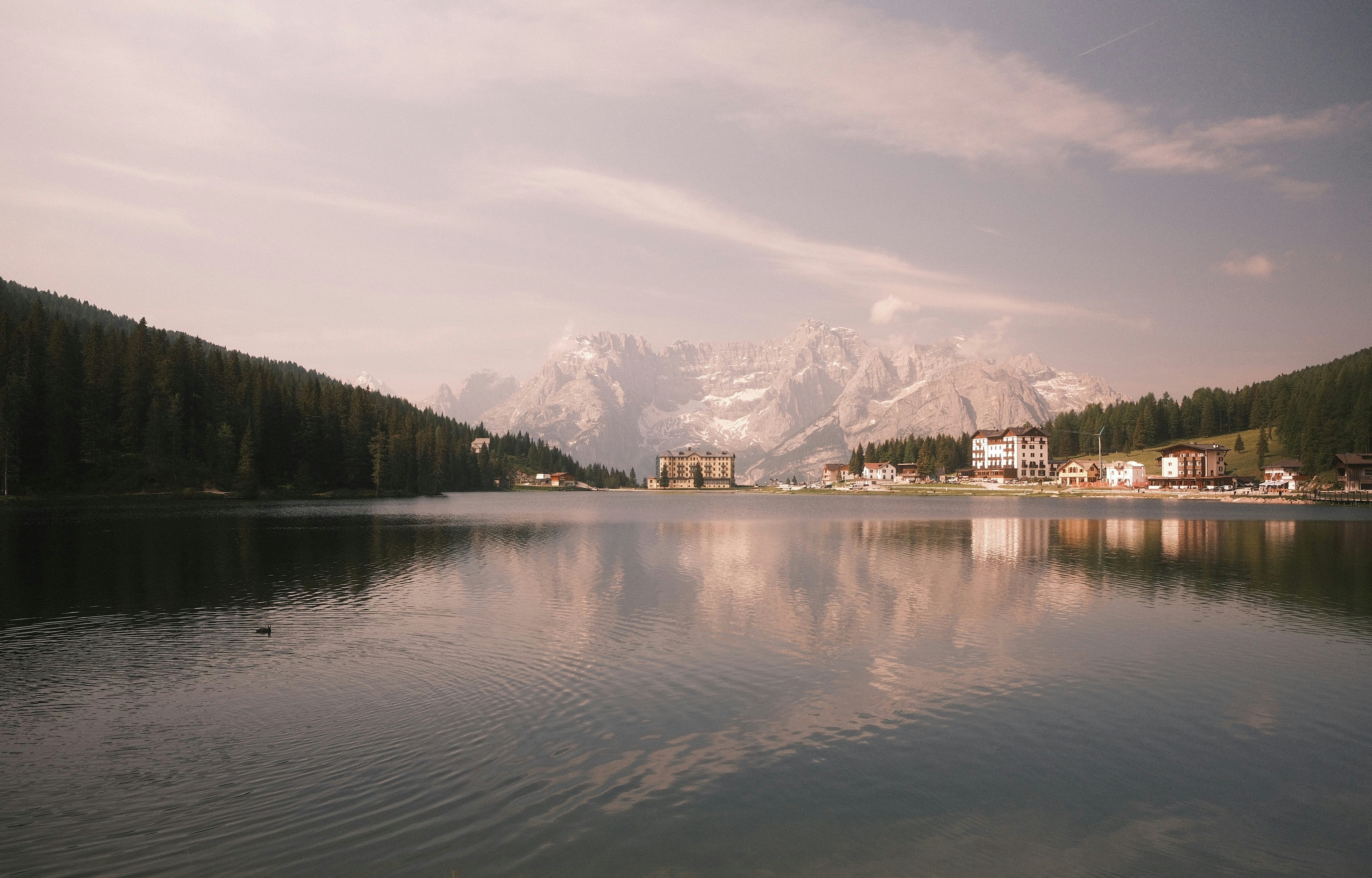 Serene lake reflecting snow-capped mountains under a pastel sky.